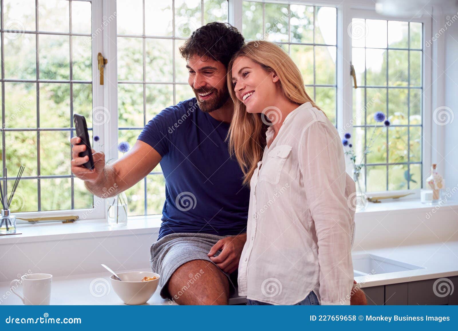 Couple Wearing Pyjamas in Kitchen Using Mobile Phone Whilst Eating ...