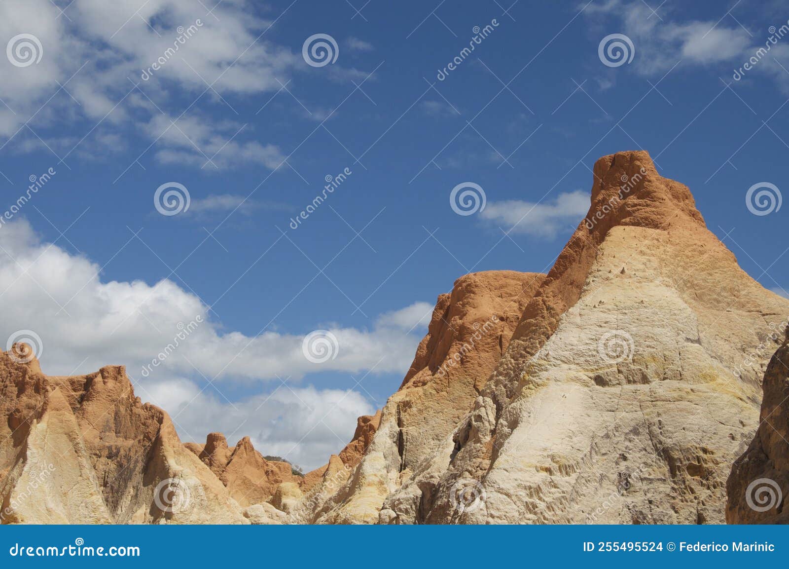 Crag of Colored Sand and White Clouds in a Blue Sky Stock Photo - Image ...