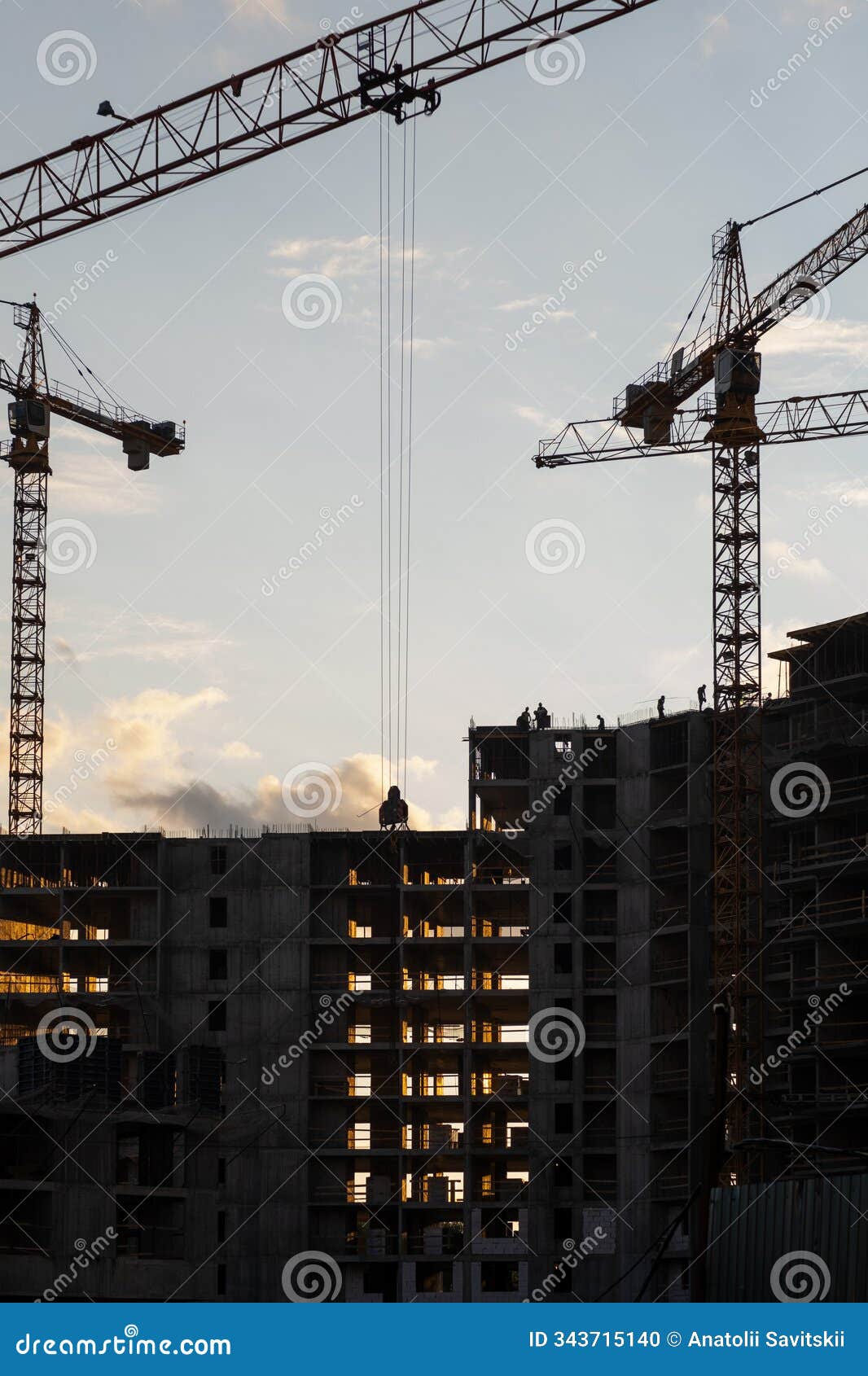 Cranes Operate at a Construction Site during Sunset, with Workers ...