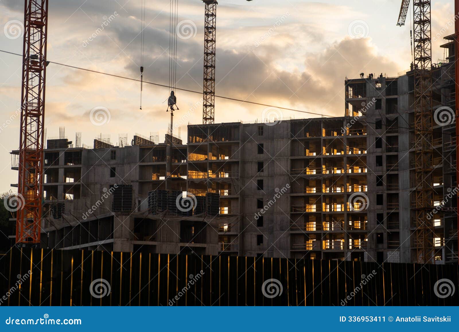 Cranes Operate at Dusk, Lifting Materials Above a Bustling Construction ...