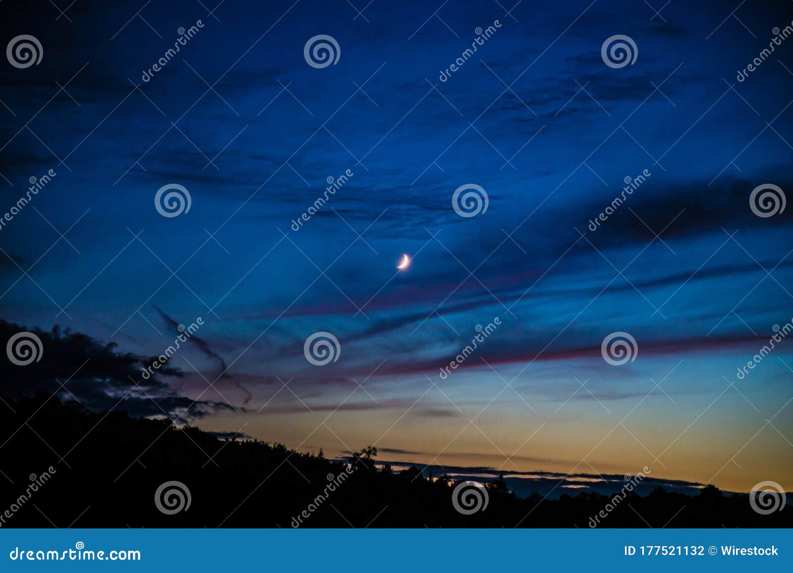Crescent Moon Against a Blue Sky with a Setting Sun in the Horizon ...