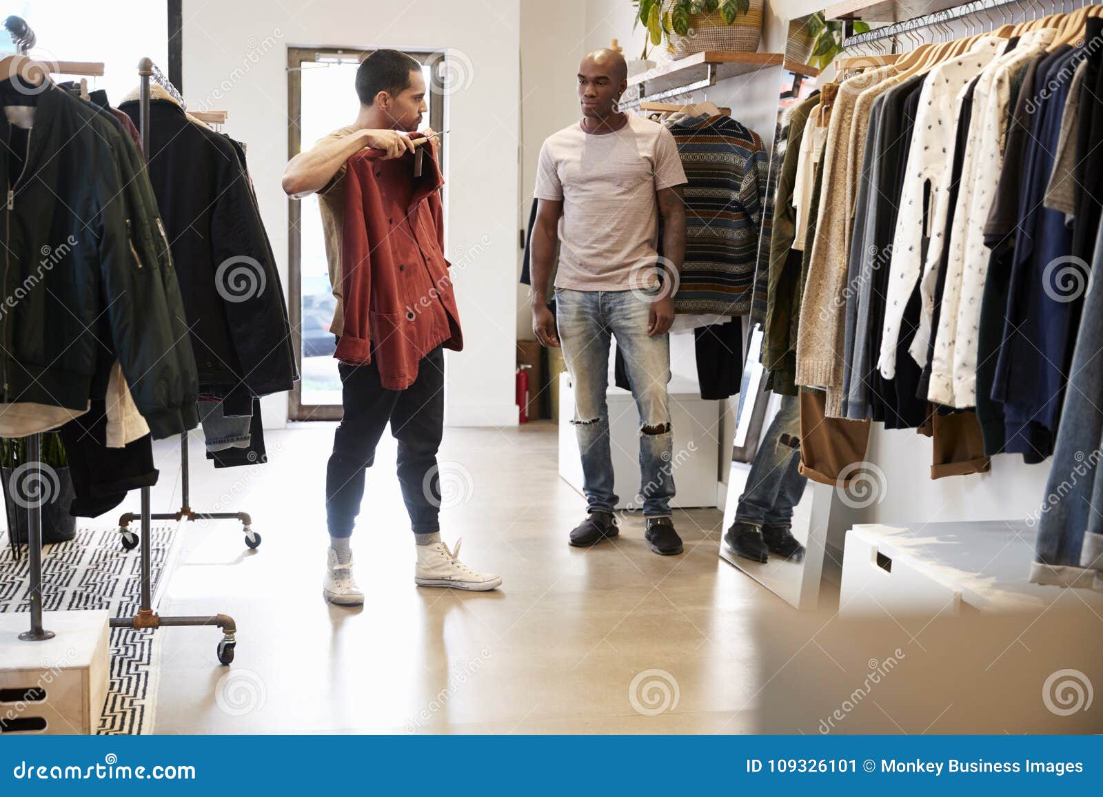 Customer Holds Up Clothes in a Shop while Assistant Looks on Stock ...