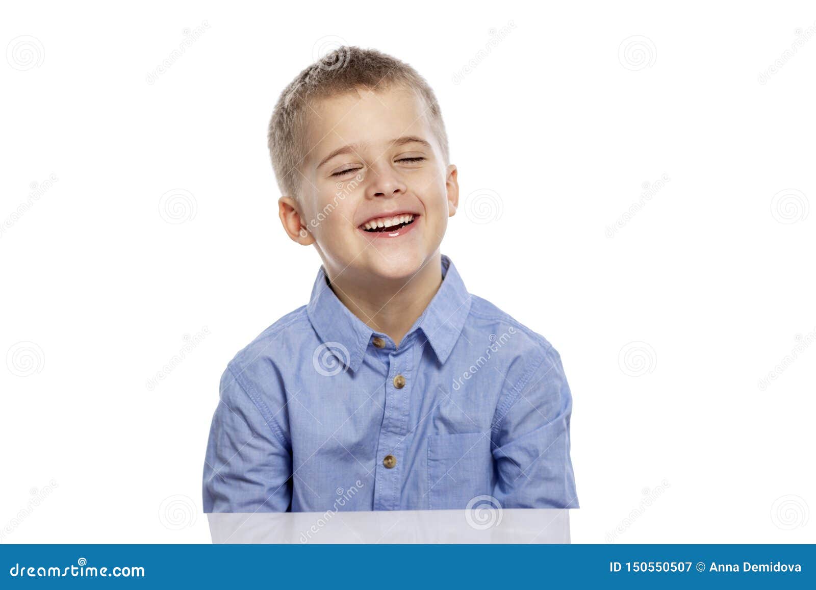 Cute Boy of School Age Sits at the Table and Laughs. Isolated on a ... Cute Boy of School Age Sits at the Table and Laughs. Isolated on a ...