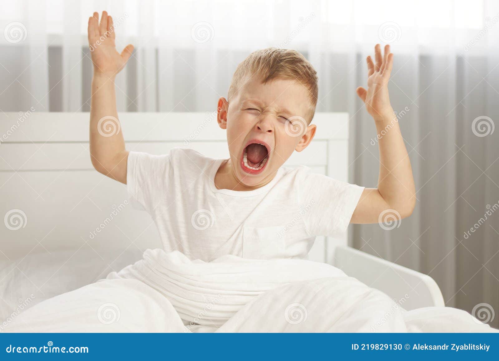 The Cute Boy Wakes Up with His Arms Outstretched and Yawns. Stock Photo ...