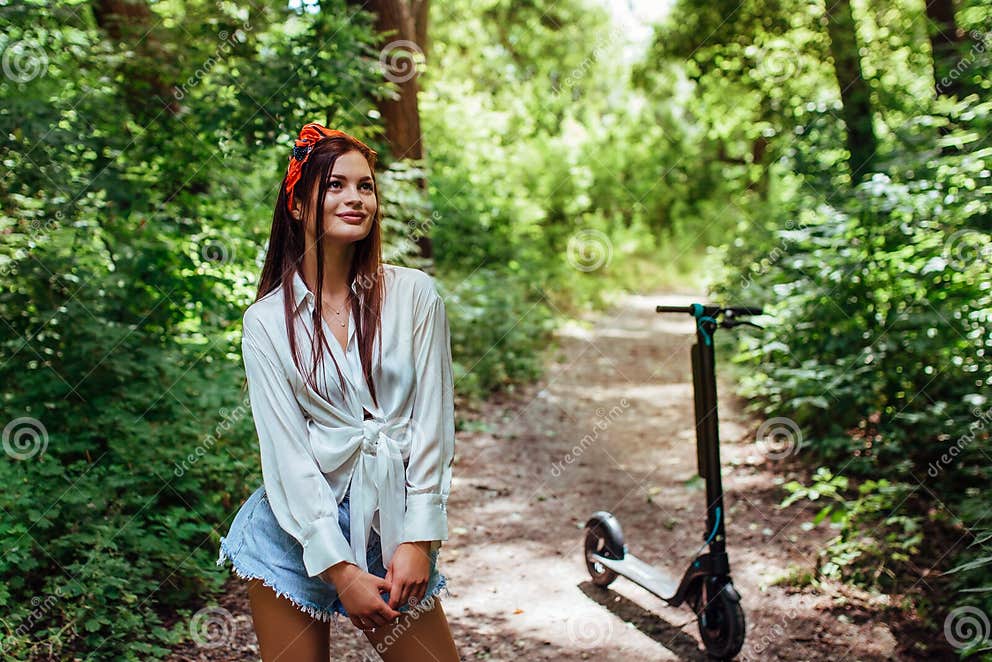 Cute Brunette Girl Rides On An Electric Scooter In The Park She Is
