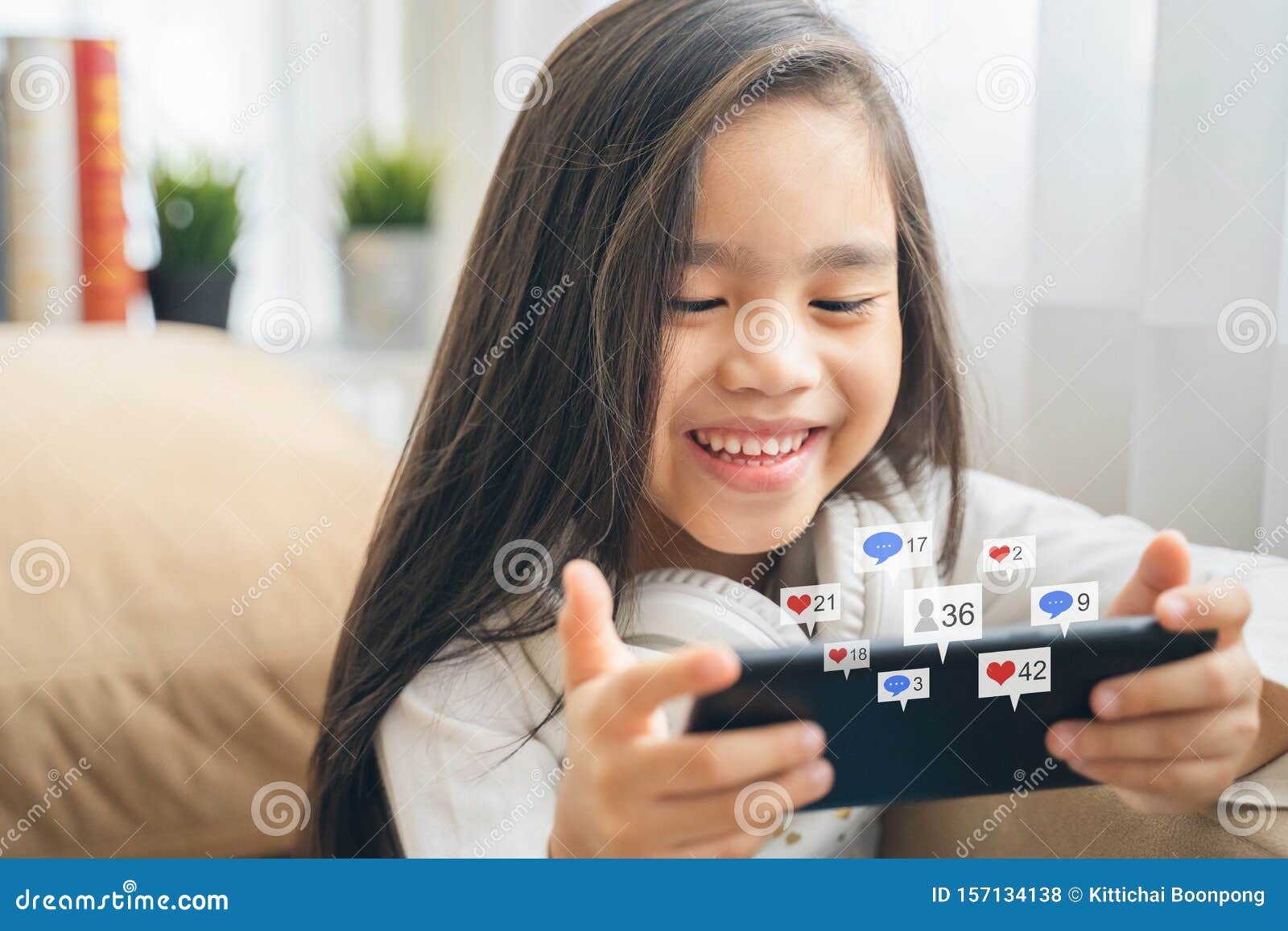 Cute Child Using a Smartphone and Smiling while Sitting on Sofa at Home ...