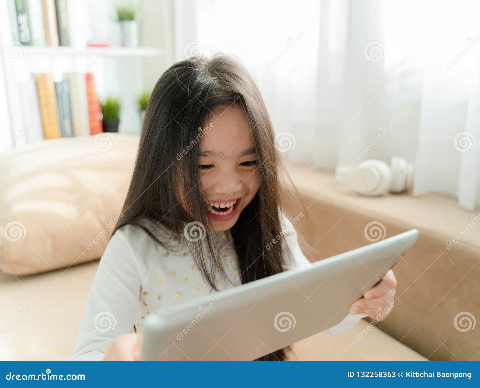 Cute Child Using a Tablet and Smiling while Sitting on Sofa at H Stock ...
