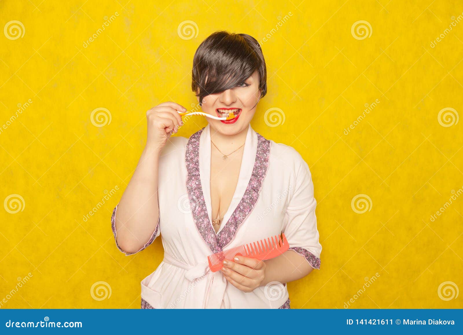 Cute Chubby Girl In A Pink Robe Stands With A Comb And Toothbrush On A