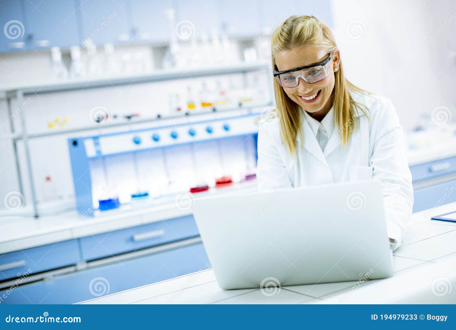 Female Researcher in White Lab Coat and Protective Goggles Using Laptop ...