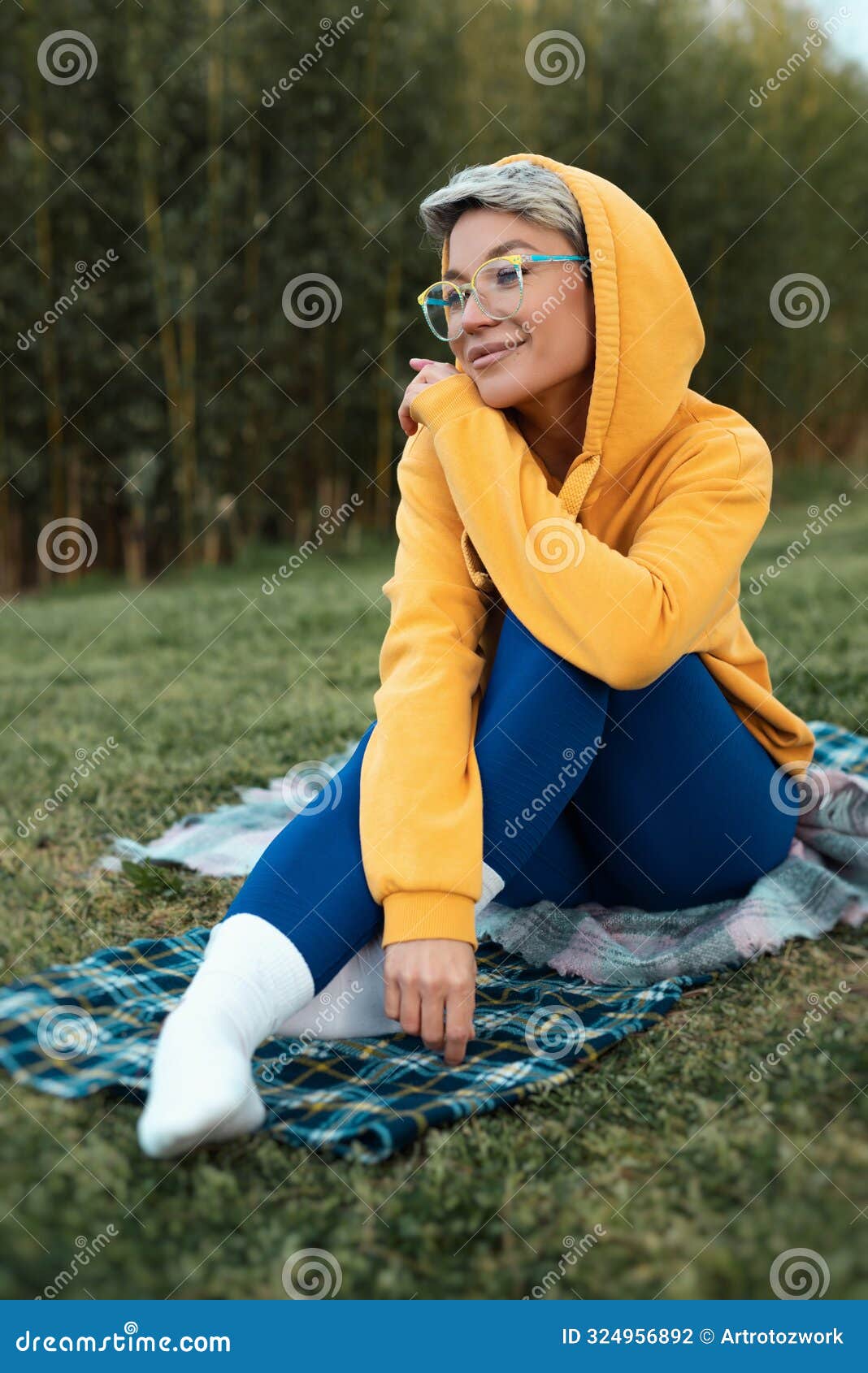Cute Girl With Glasses In An Orange Hoodie Is Sitting In A Park In