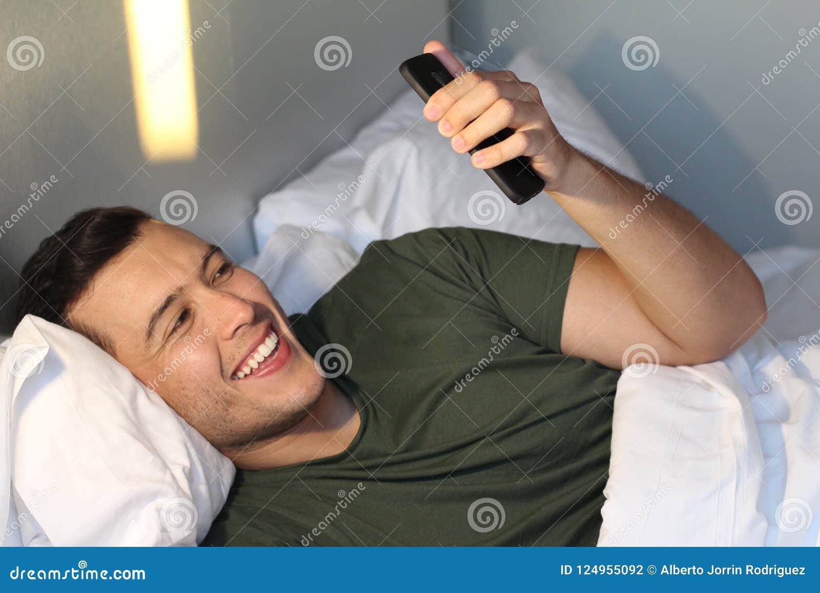 Cute Guy Comfortably Using Phone in Bed Stock Photo - Image of happy ...