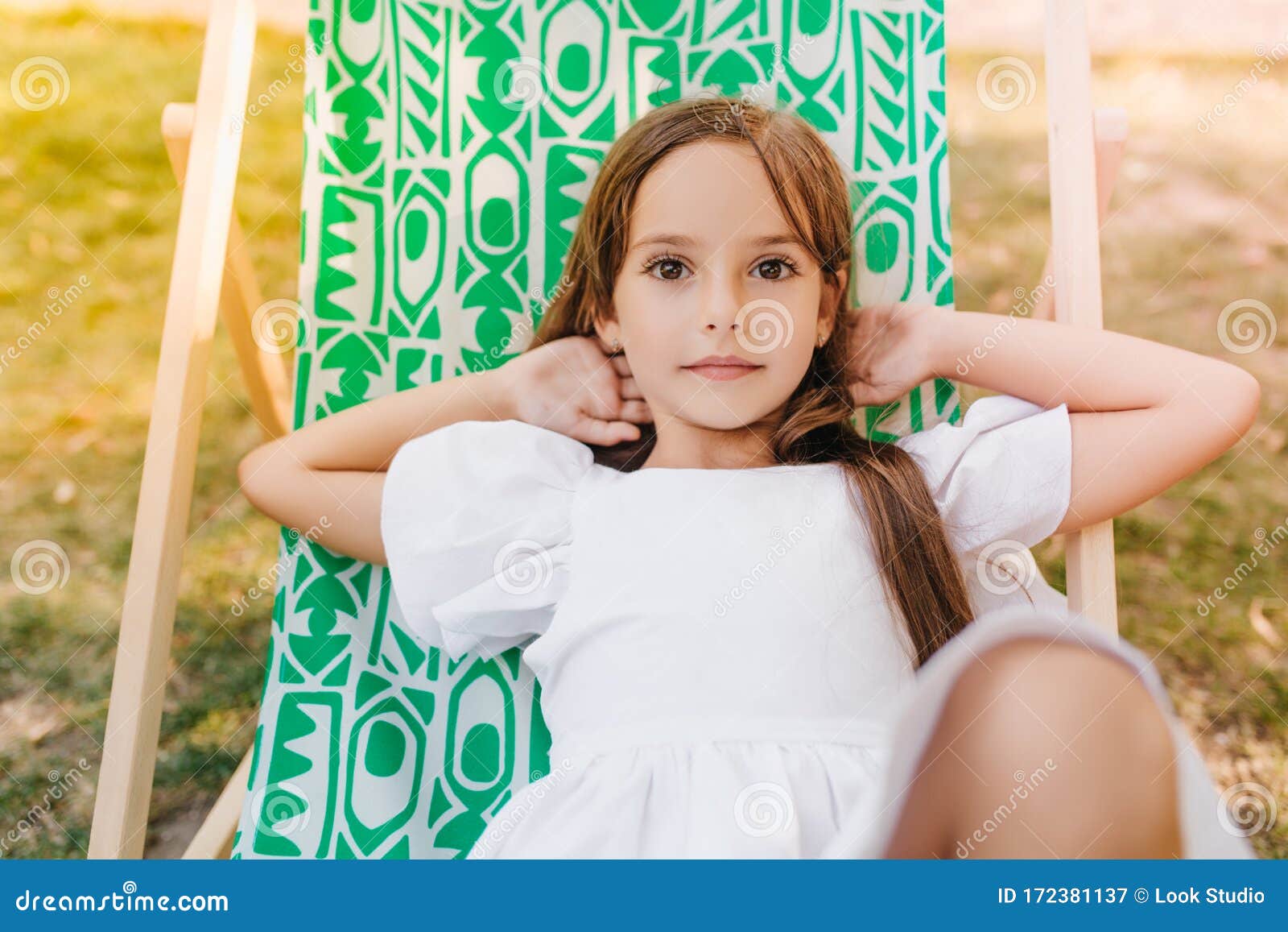 Cute Lightly Tanned Girl In White Dress Resting In Green Chaise Longue