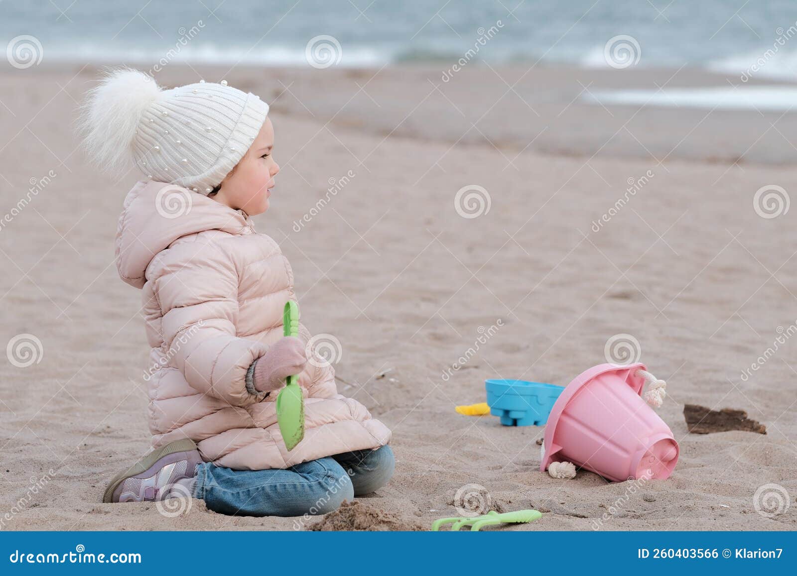 Cute Little Girl is Digging in the Sand on a Cold Day at the Beach ...