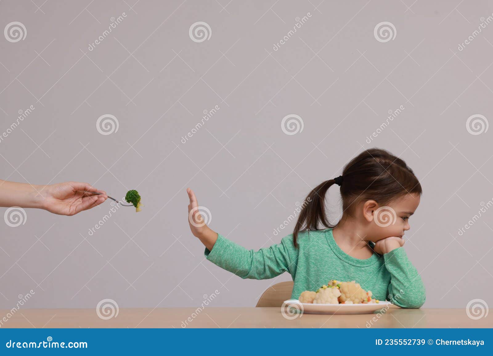 Cute Little Girl Refusing To Eat Vegetables at Table on Grey Background ...