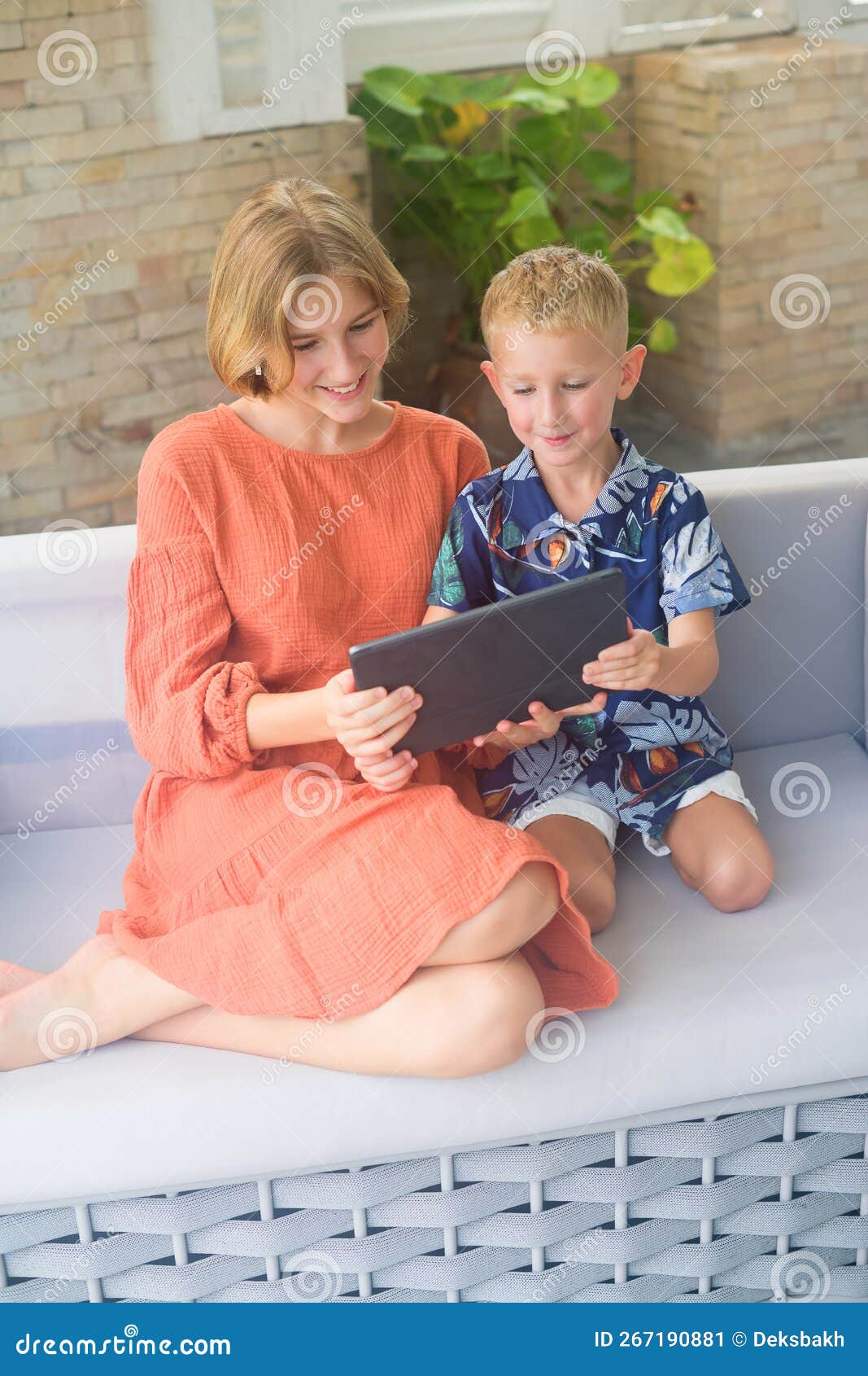 Cute Siblings Brother And Sister Sitting On Sofa At Home And Playing On Wireless Tablet Together