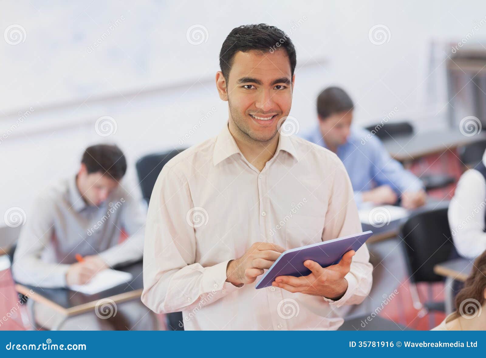 Cute Teacher Holding His Tablet while Posing in His Classroom Stock ...