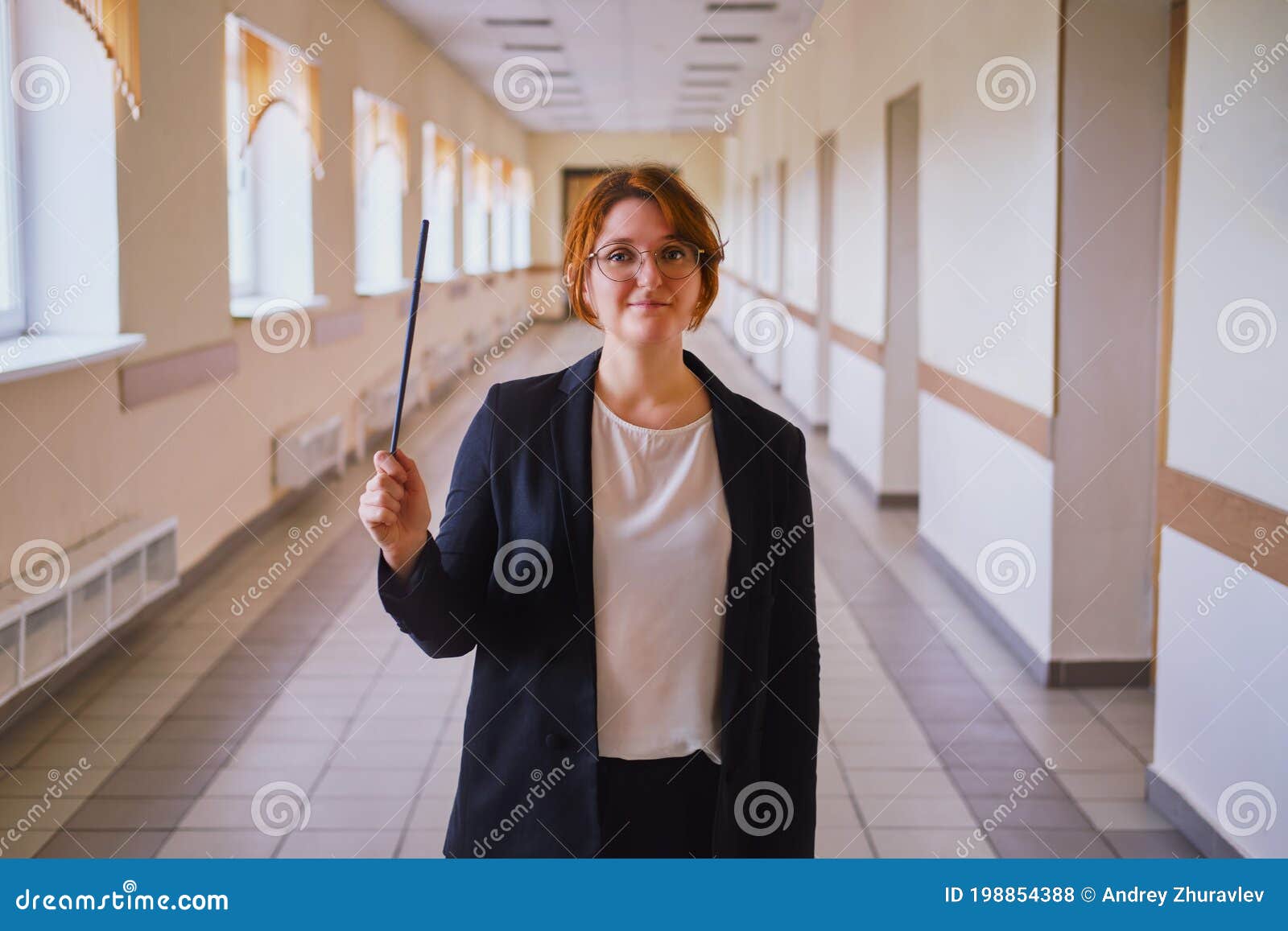 Cute Teacher is Smiling while Standing in an Empty School Corridor with ...