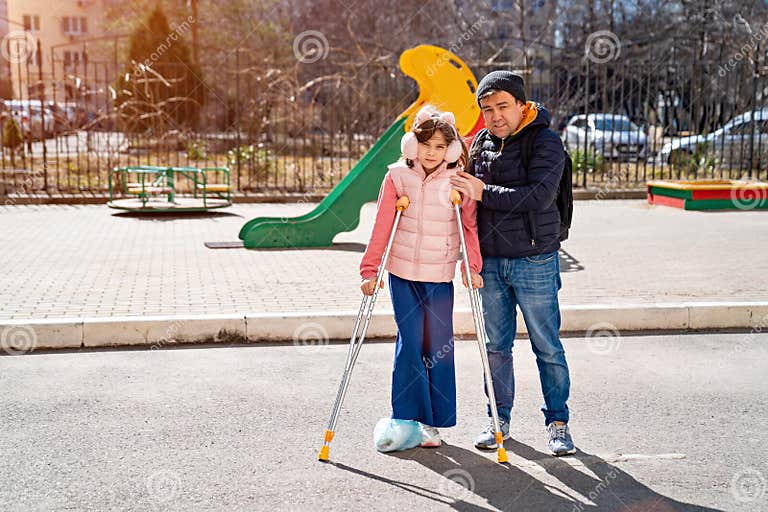 Dad Helps Daughter Learn To Walk On Crutches Plaster On Your Feet