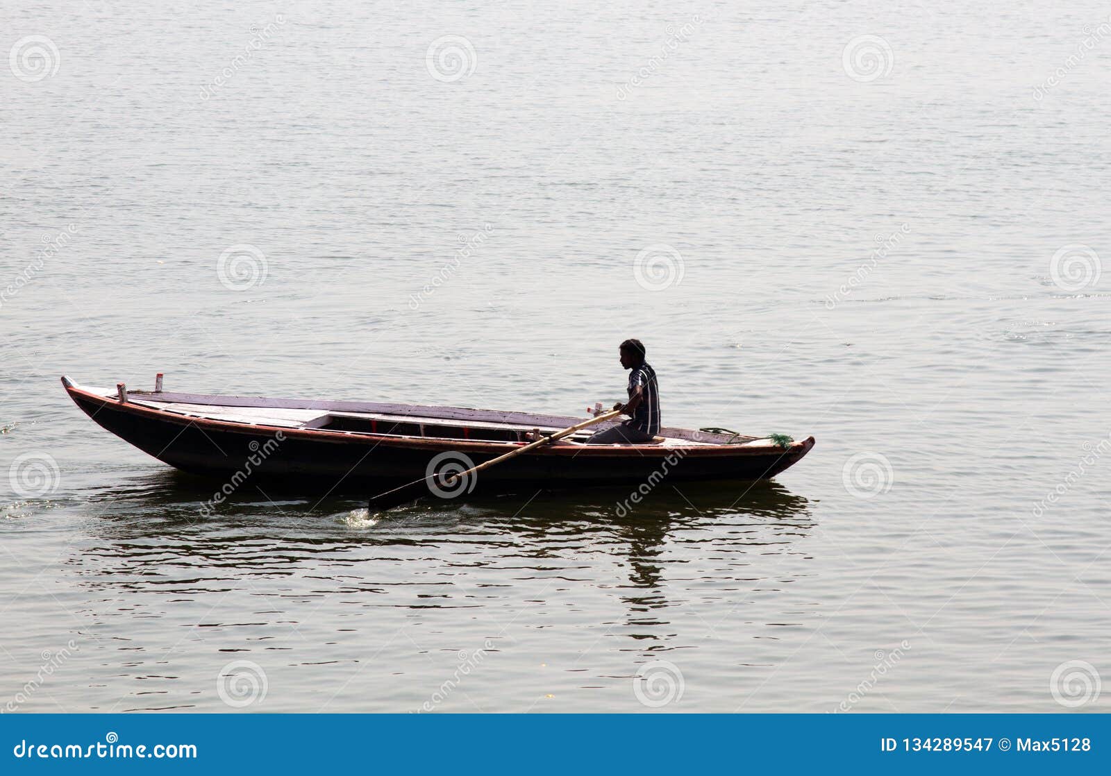 Indian Waterman Standing In The Front Of Boat And See The Varanasi ...