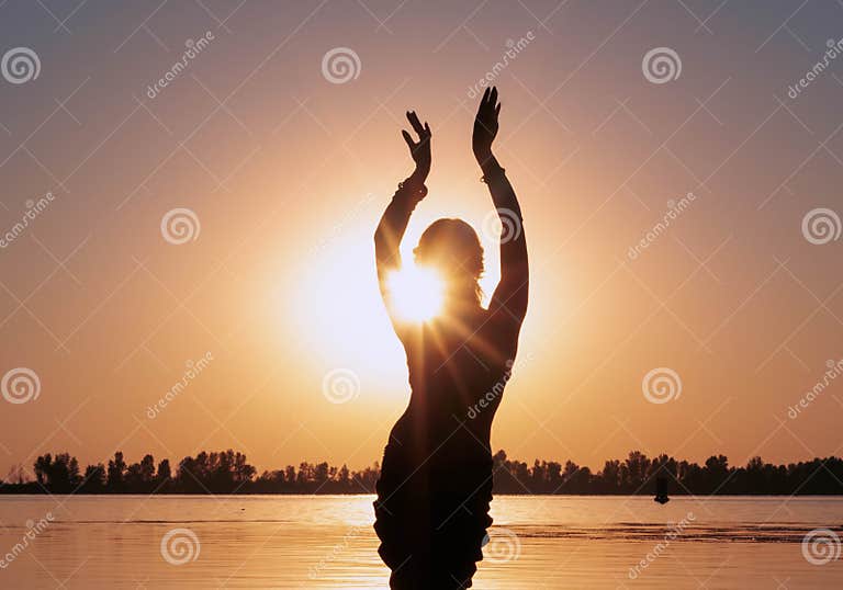 Dark Glowing Silhouette Of Slim Woman With Hands Up Near Big River