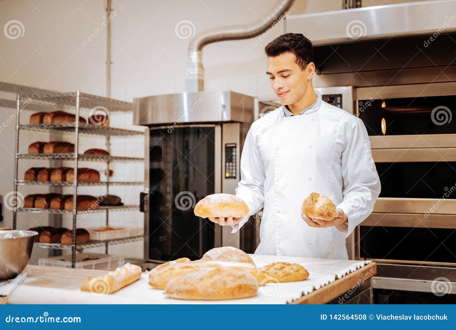 Dark-haired Satisfied Baker Holding Two Loafs of Bread in His Hands ...