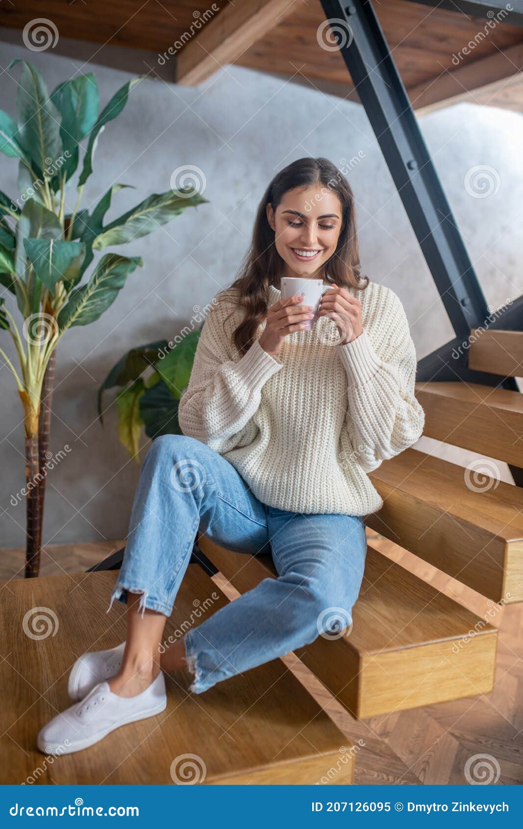 Young Dark Haired Pretty Woman In Jeans And White Sweater Sitting On