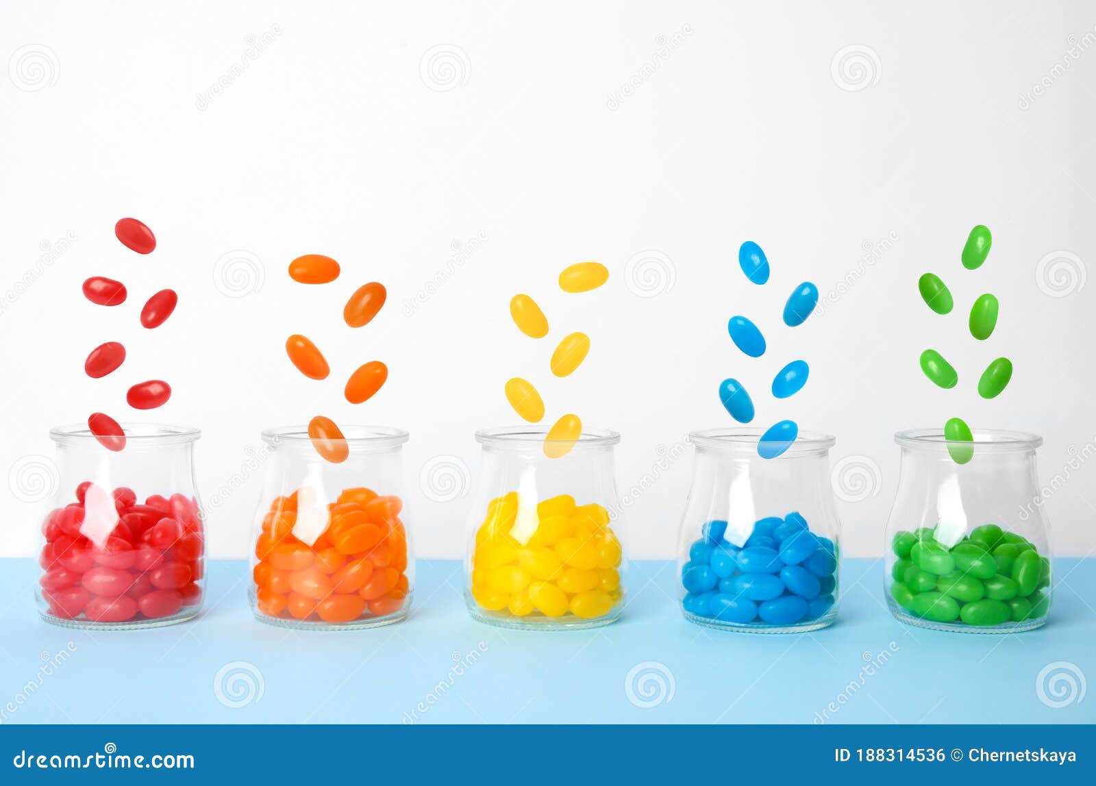 Delicious Color Jelly Beans Falling into Jars on Blue Table Stock Photo ...