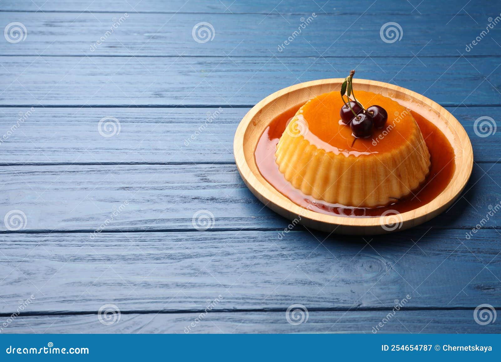 Delicious Pudding with Caramel and Cherries on Blue Wooden Table. Space ...