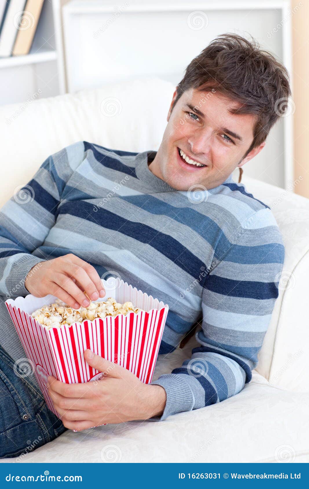 Delighted Young Man Eating Popcorn Lying on a Sofa Stock Image - Image ...