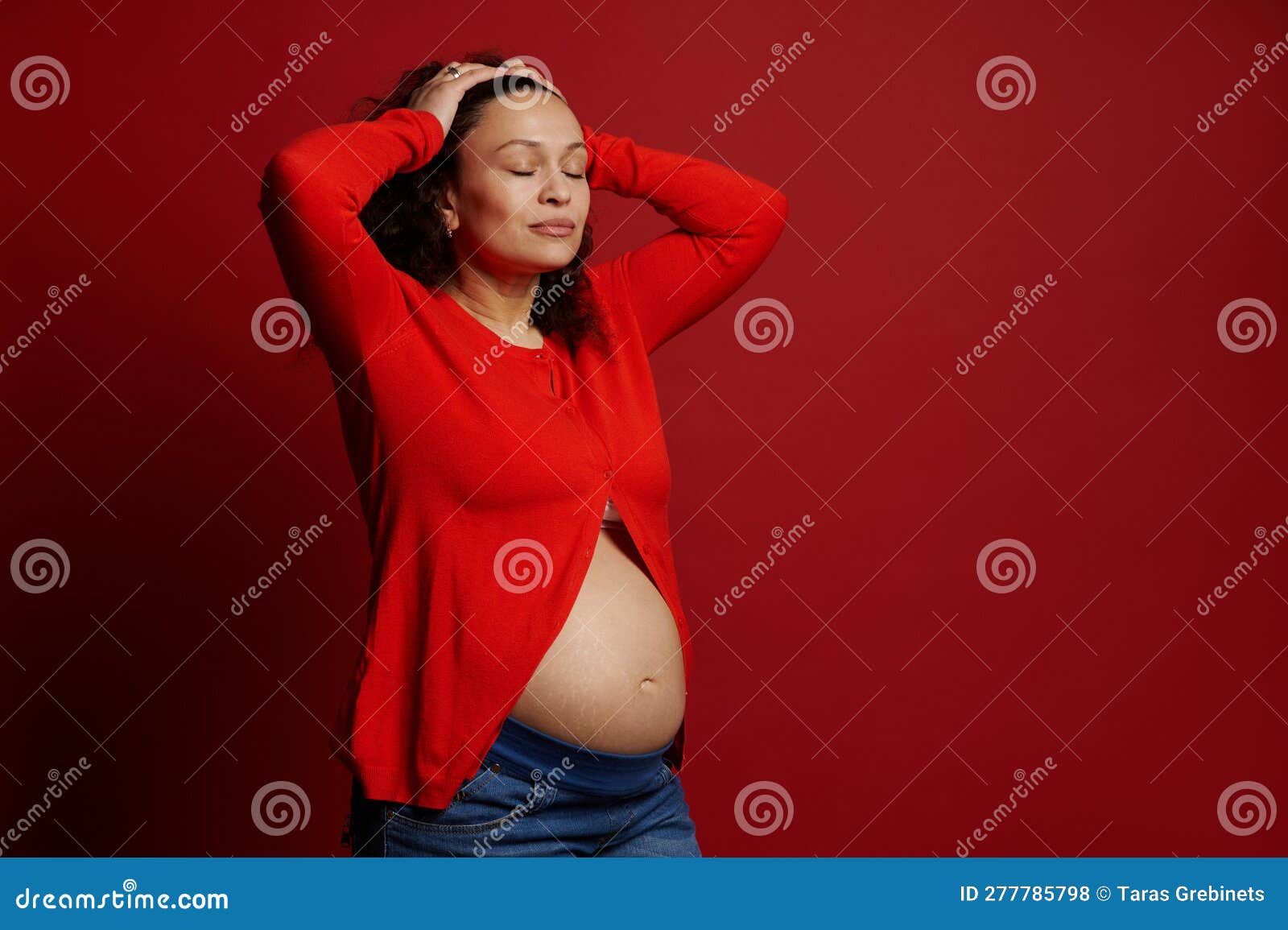 Delightful Pregnant Woman Posing With Closed Eyes And Bare Belly On Red