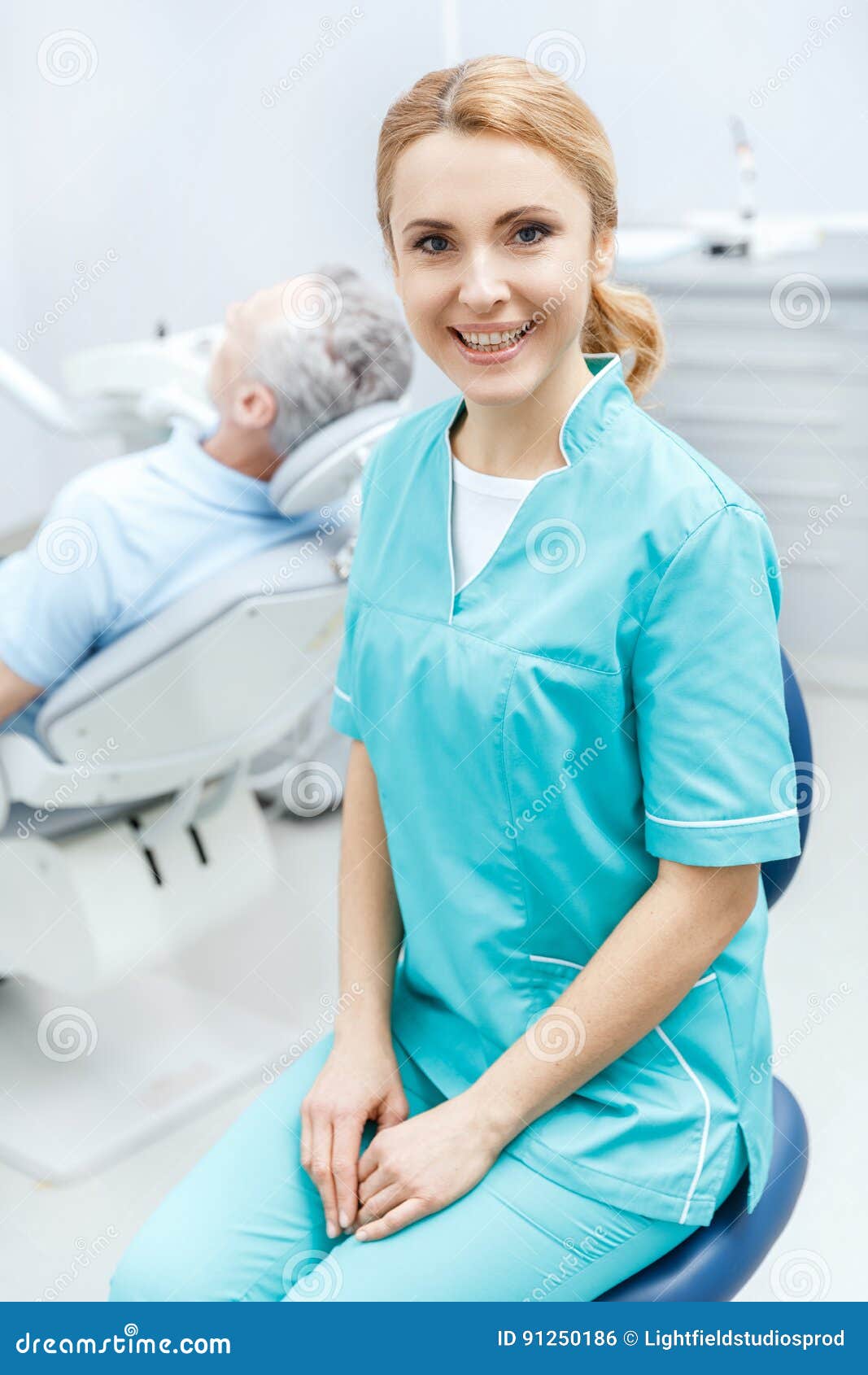 Dentist In Medical Uniform Sitting In Clinic And Smiling At Camera