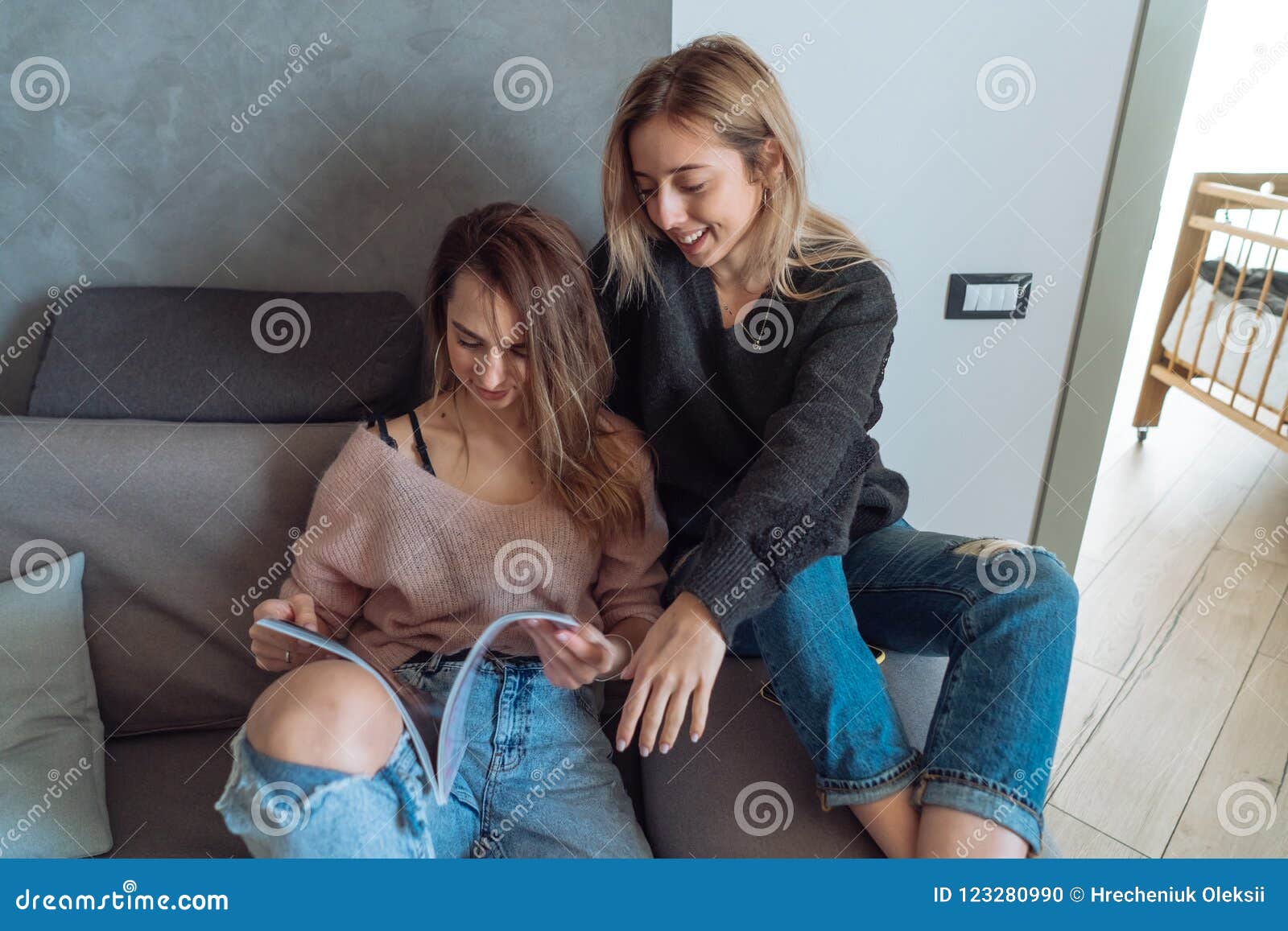 Deux Jeunes Filles Sur Une Magazine De Observation De Divan Photo Stock