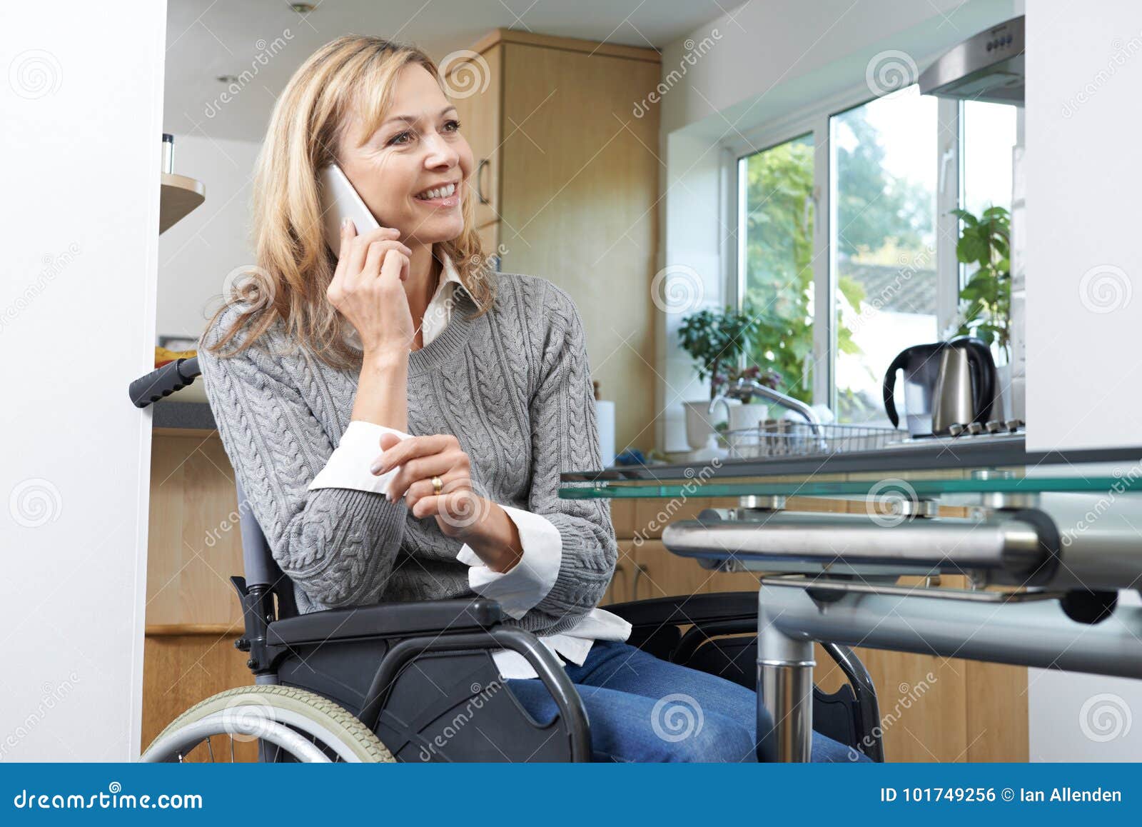 Disabled Woman In Wheelchair Talking On Mobile Phone At Home Stock