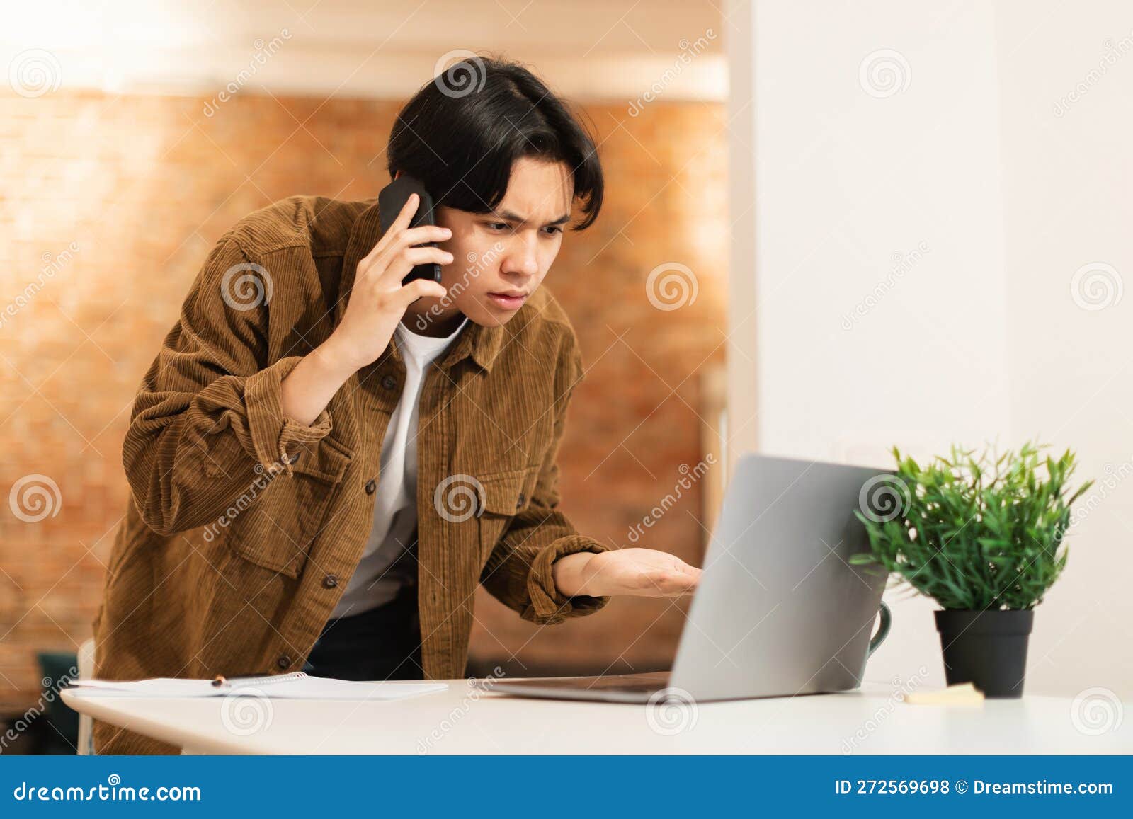 Asian Guy Talking on Phone Having Problems with Laptop Indoors Stock ...