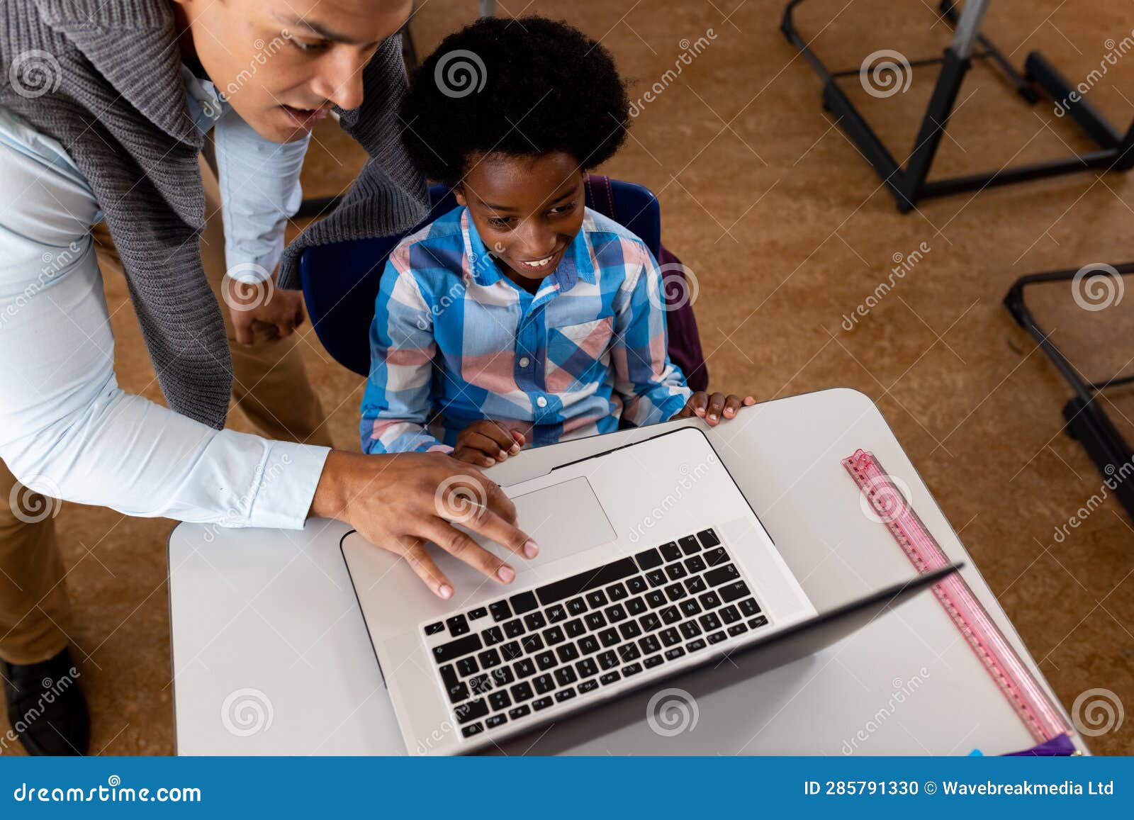 Diverse Male Teacher Using Laptop Teaching Boy at Desk in Elementary ...