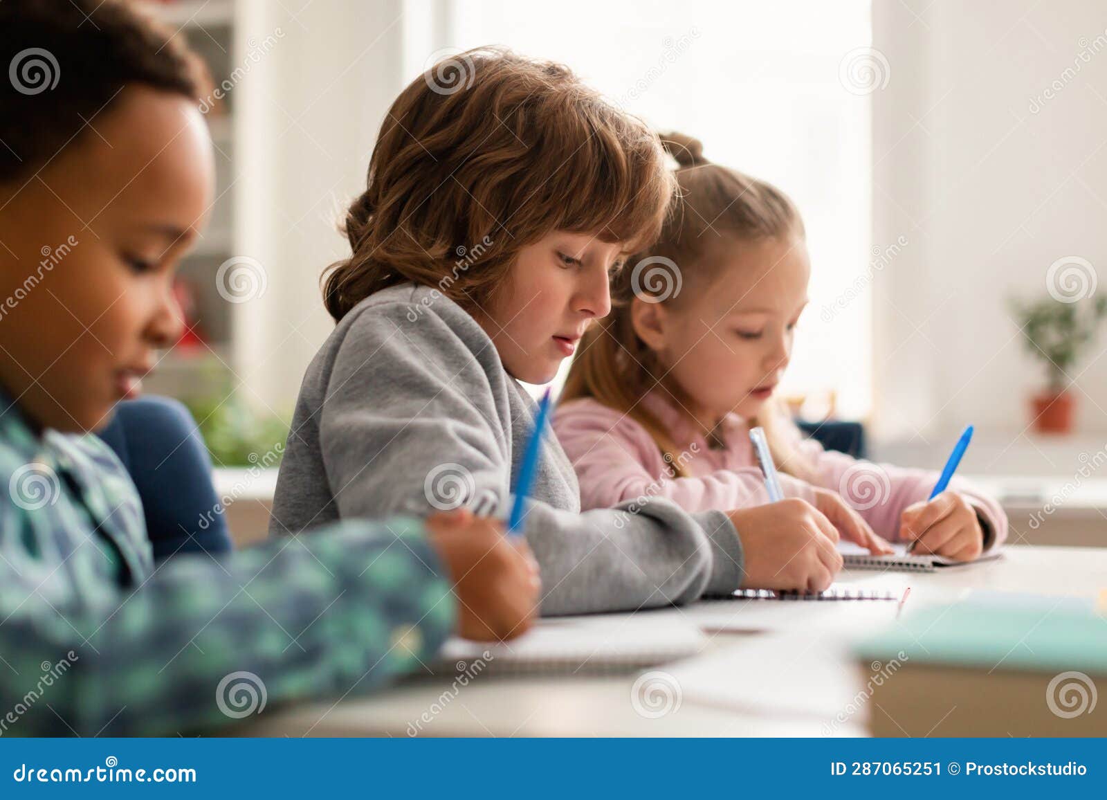 Diverse Pupil Writing during the Lesson at Desk in Classroom at ...