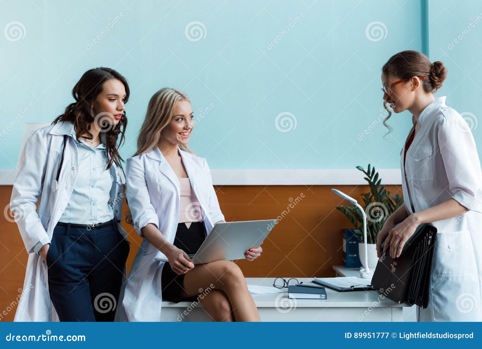 Doctor Closing Briefcase while Colleagues Using Laptop at Workplace ...