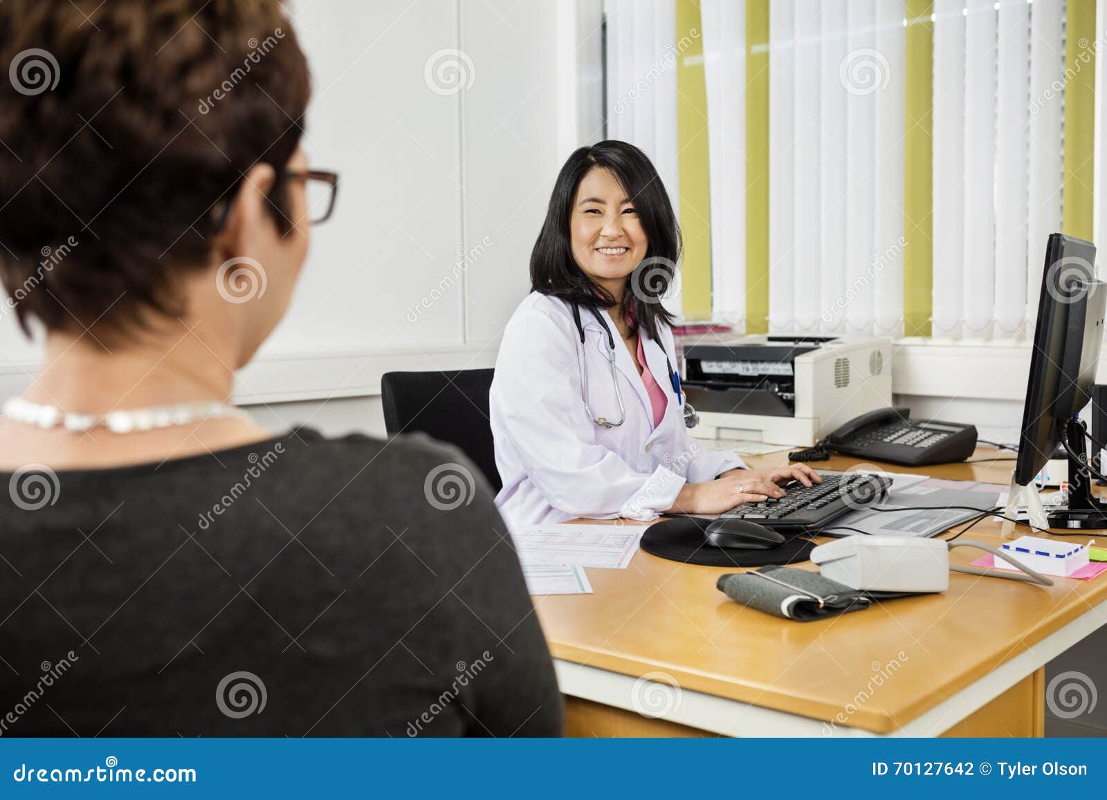 Doctor Using Computer while Looking at Patient at Desk Stock Photo ...