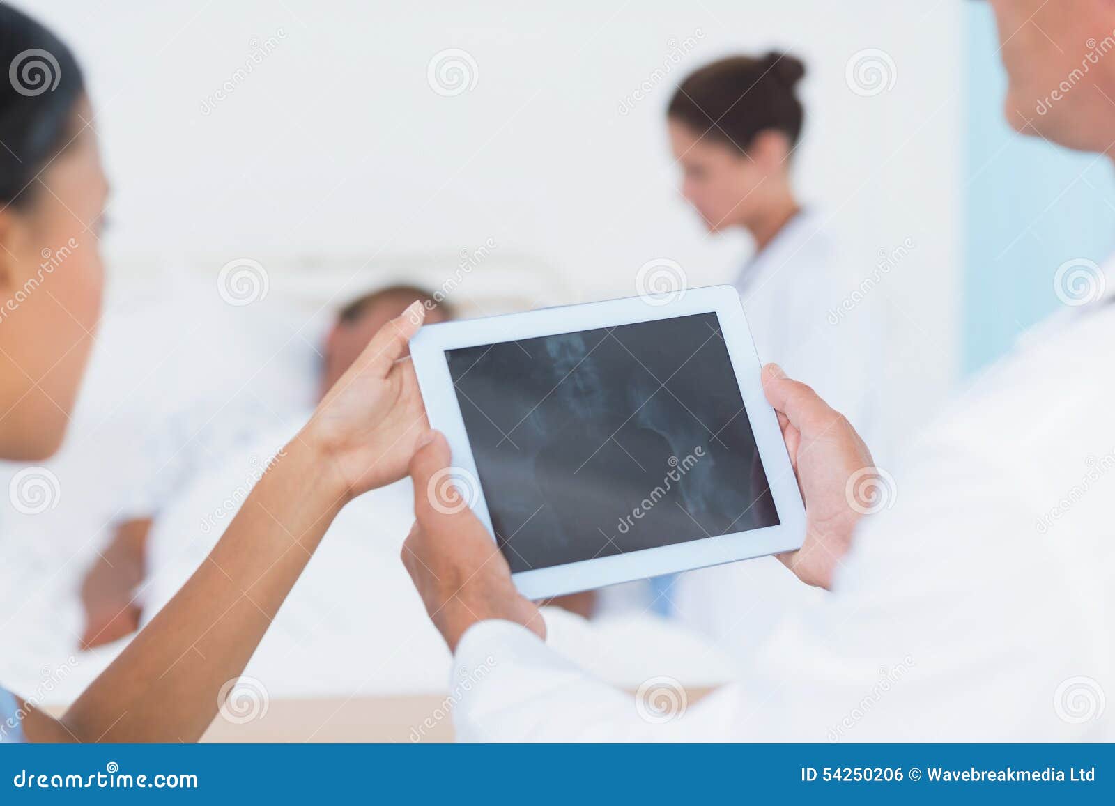 Doctor Using Digital Tablet with Colleagues and Patient Behind Stock ...