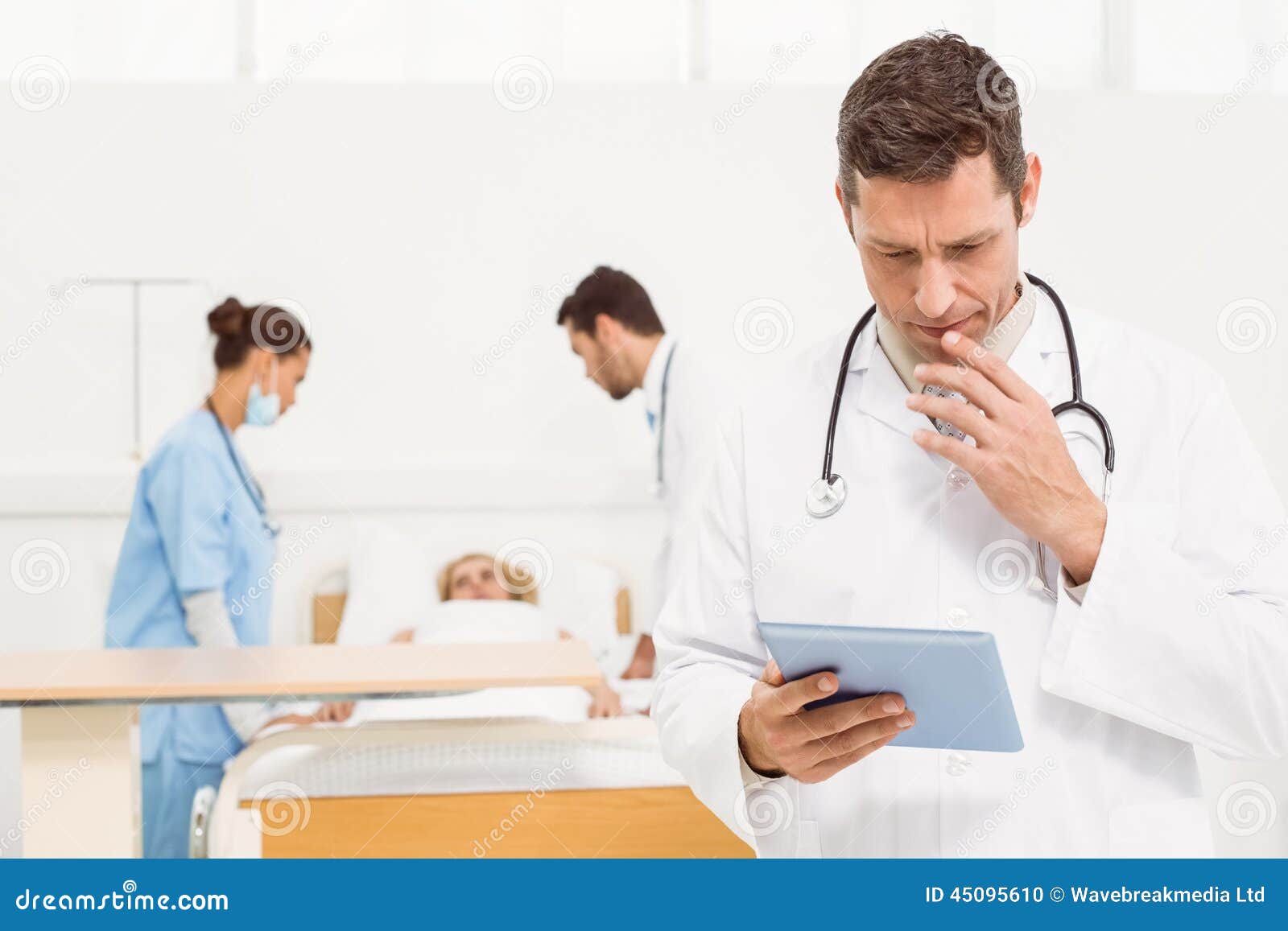 Doctor Using Digital Tablet with Colleagues and Patient Behind Stock ...