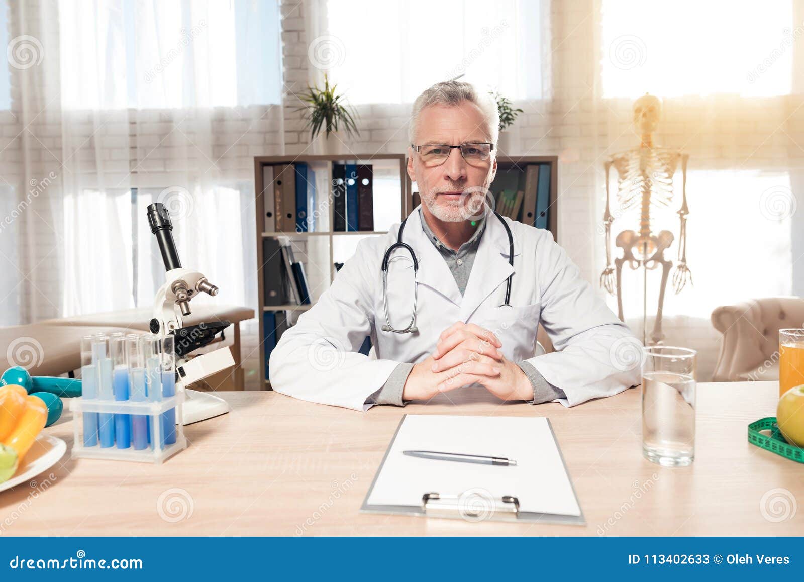 Doctor Sitting at Desk in Office with Microscope, Stethoscope and ...