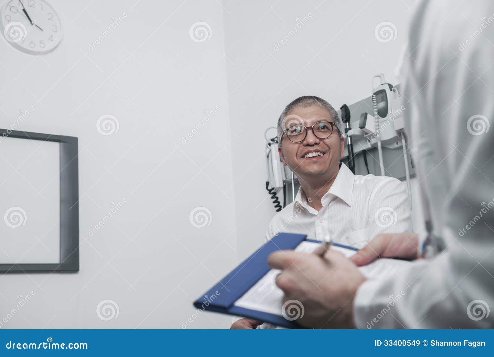 Doctor Writing on Medical Chart with a Smiling Patient Stock Image ...
