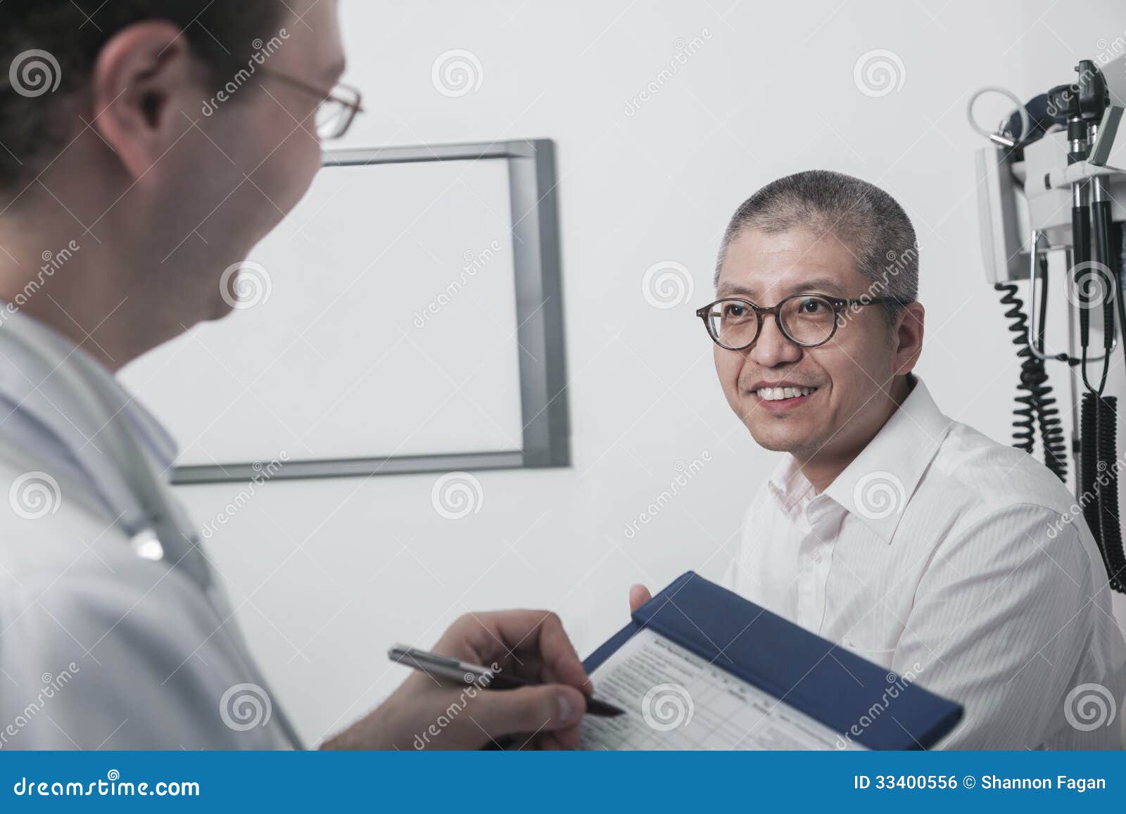 Doctor Writing on Medical Chart with a Smiling Patient Stock Photo ...