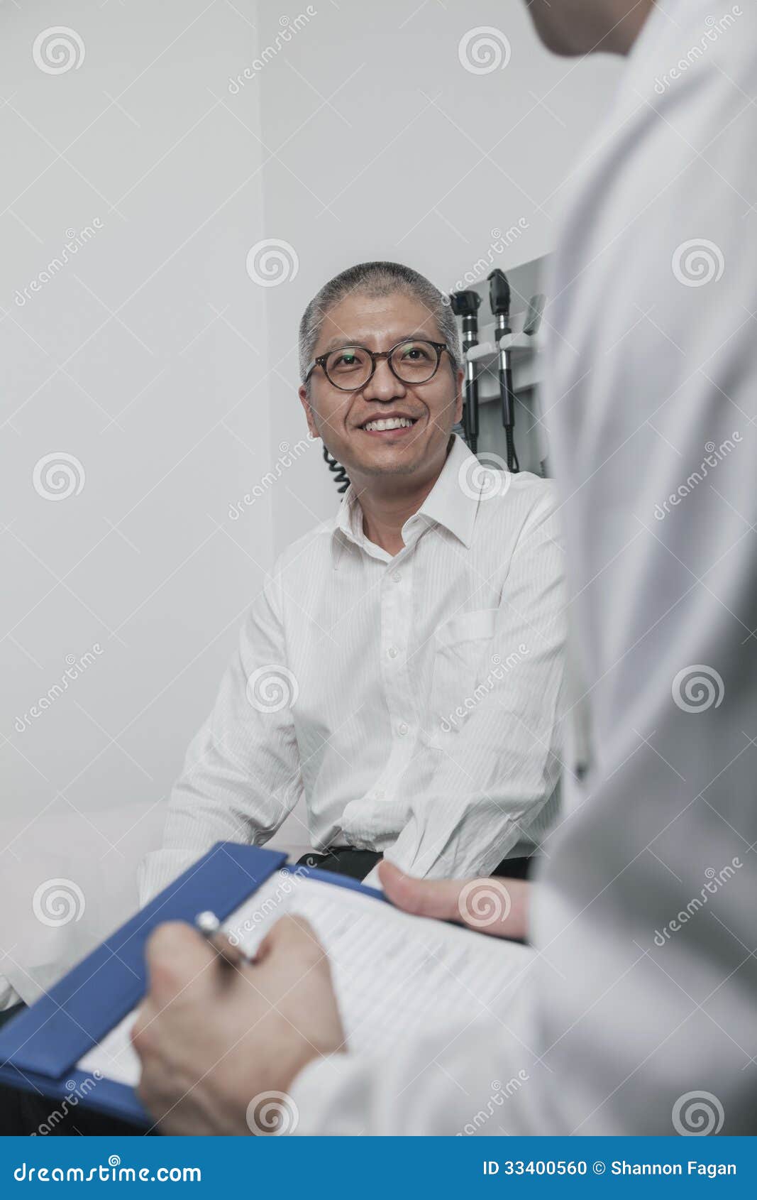 Doctor Writing on Medical Chart with a Smiling Patient Stock Photo ...