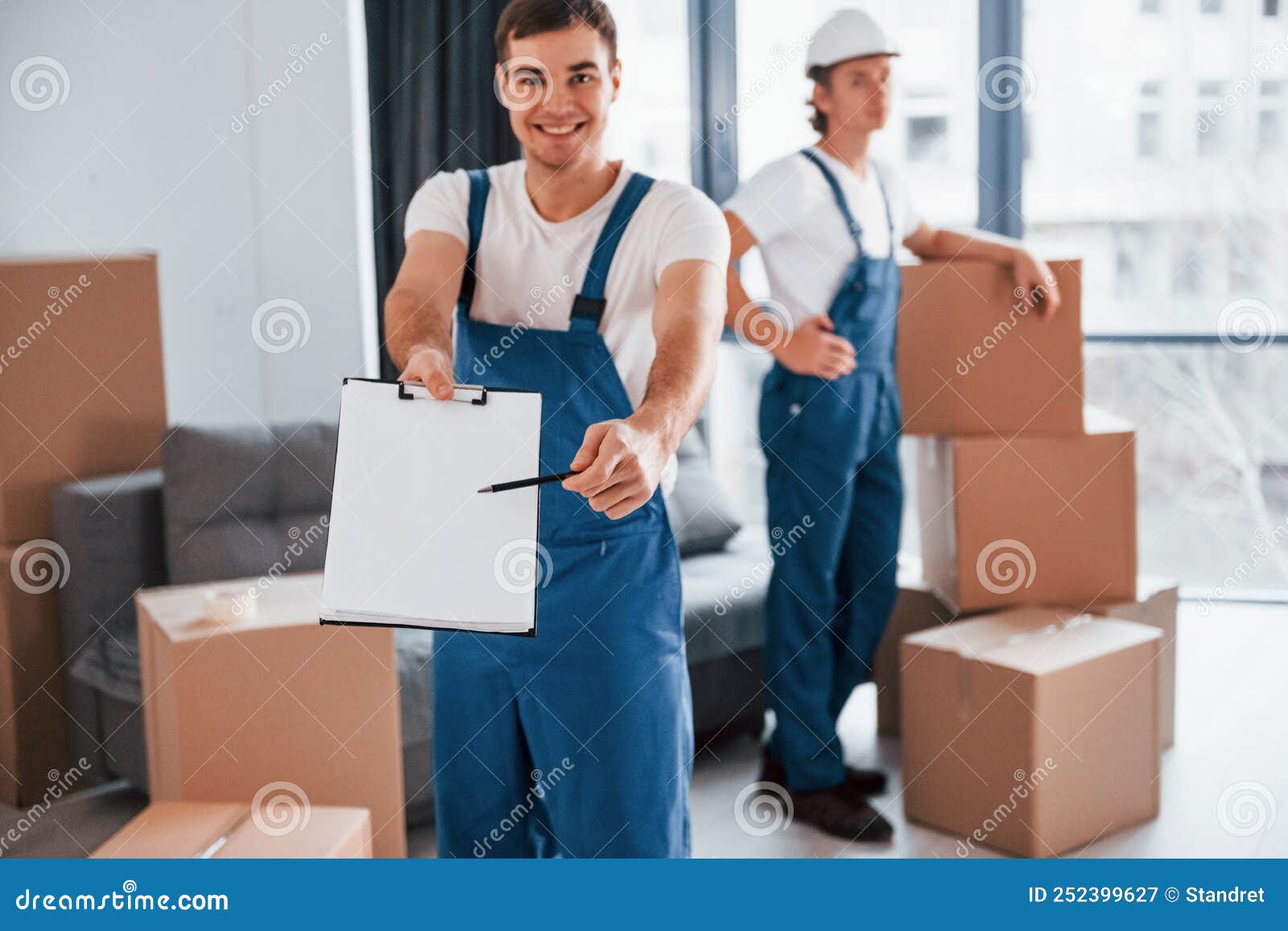 Document To Sign. Two Young Movers in Blue Uniform Working Indoors in ...