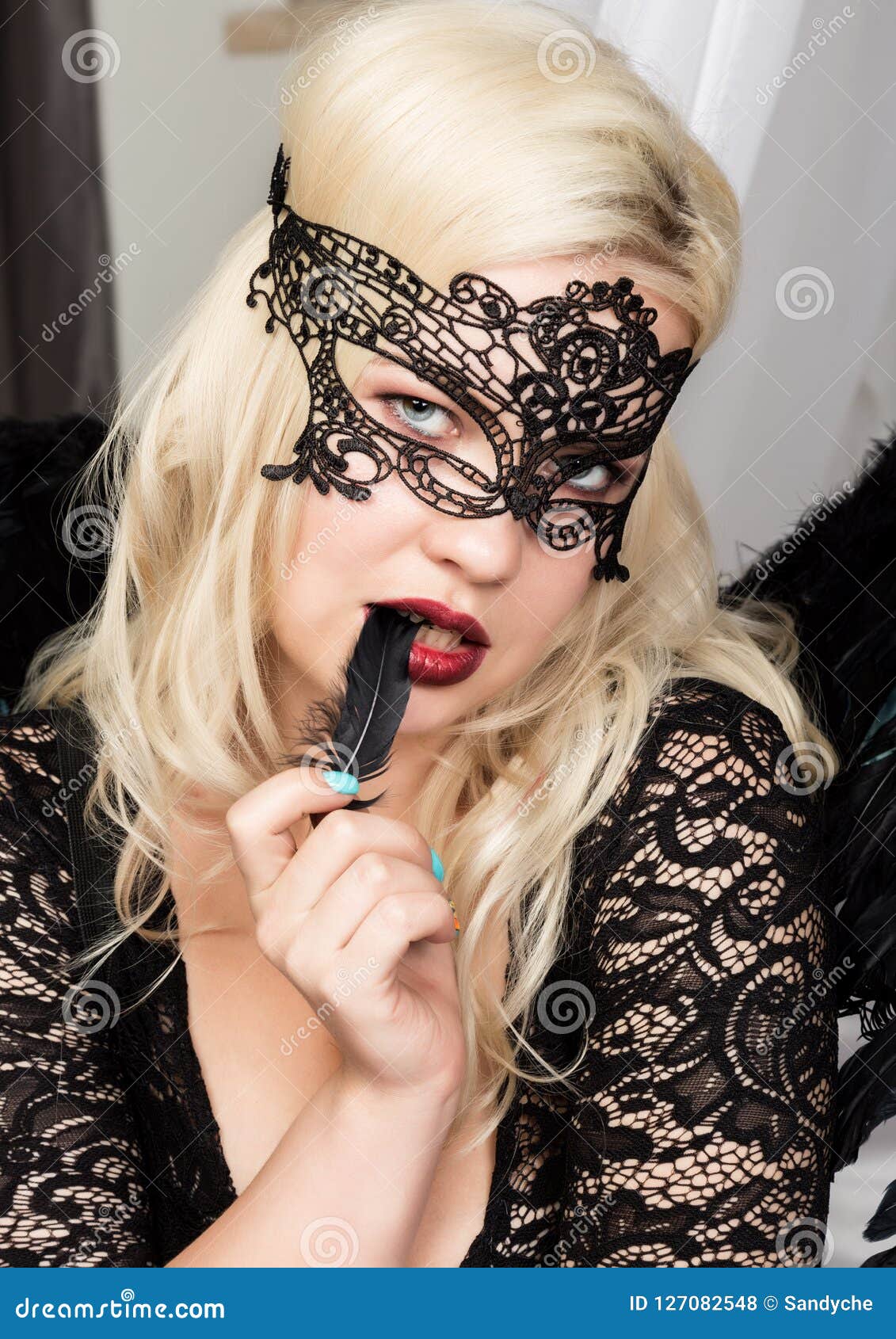 Donna Bionda Sexy In Una Maschera Del Pizzo Che Tiene Una Piuma Nera