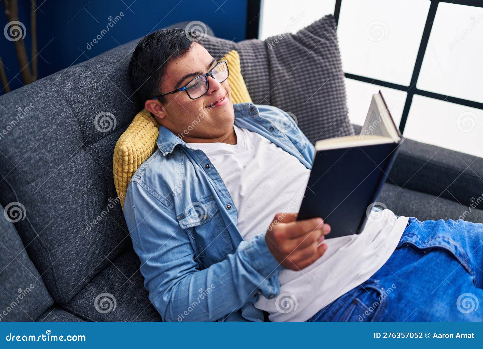 Down Syndrome Man Reading Book Lying on Sofa at Home Stock Photo ...