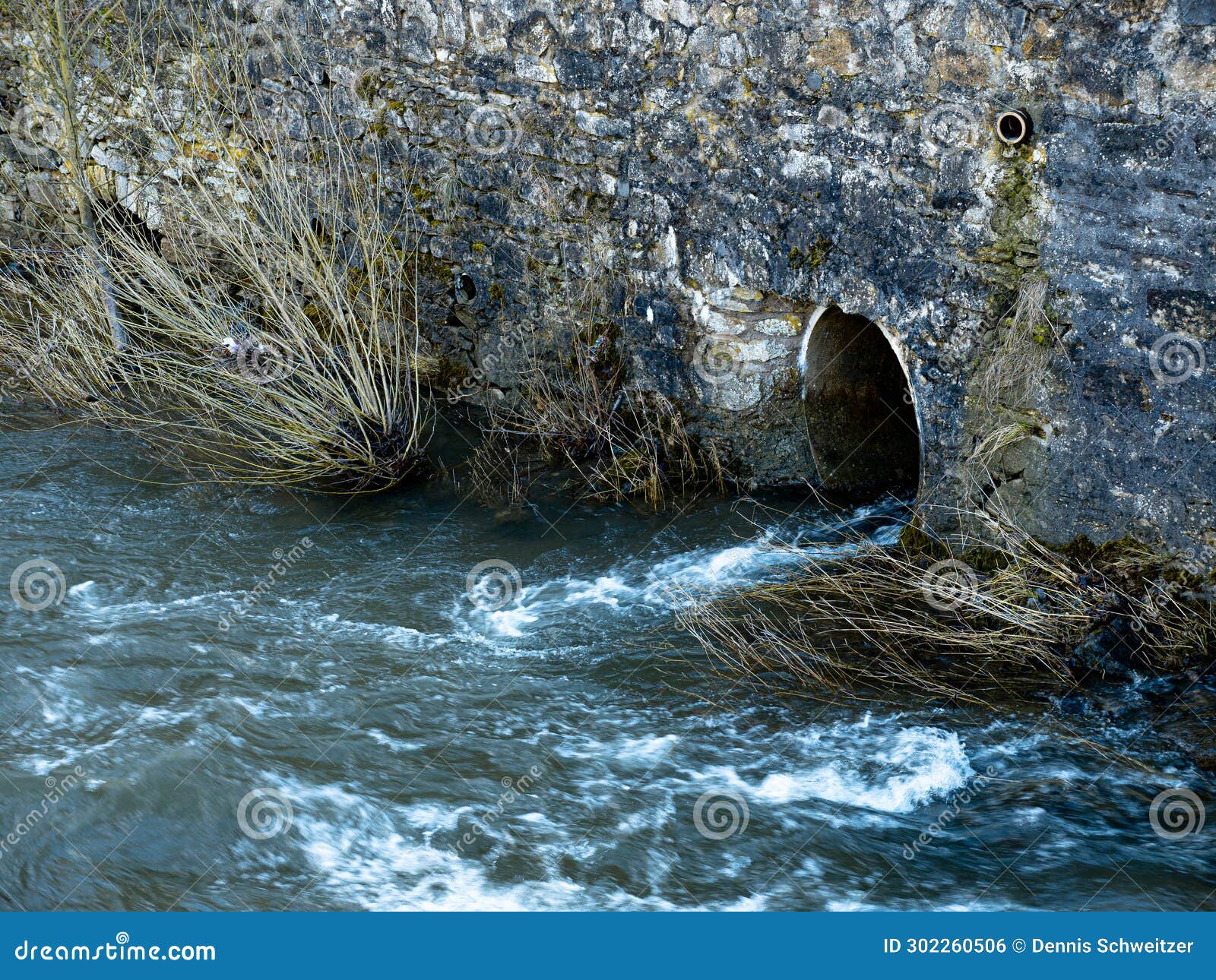A Drain that is Embedded in a Wall and Flows into a River Stock Photo ...