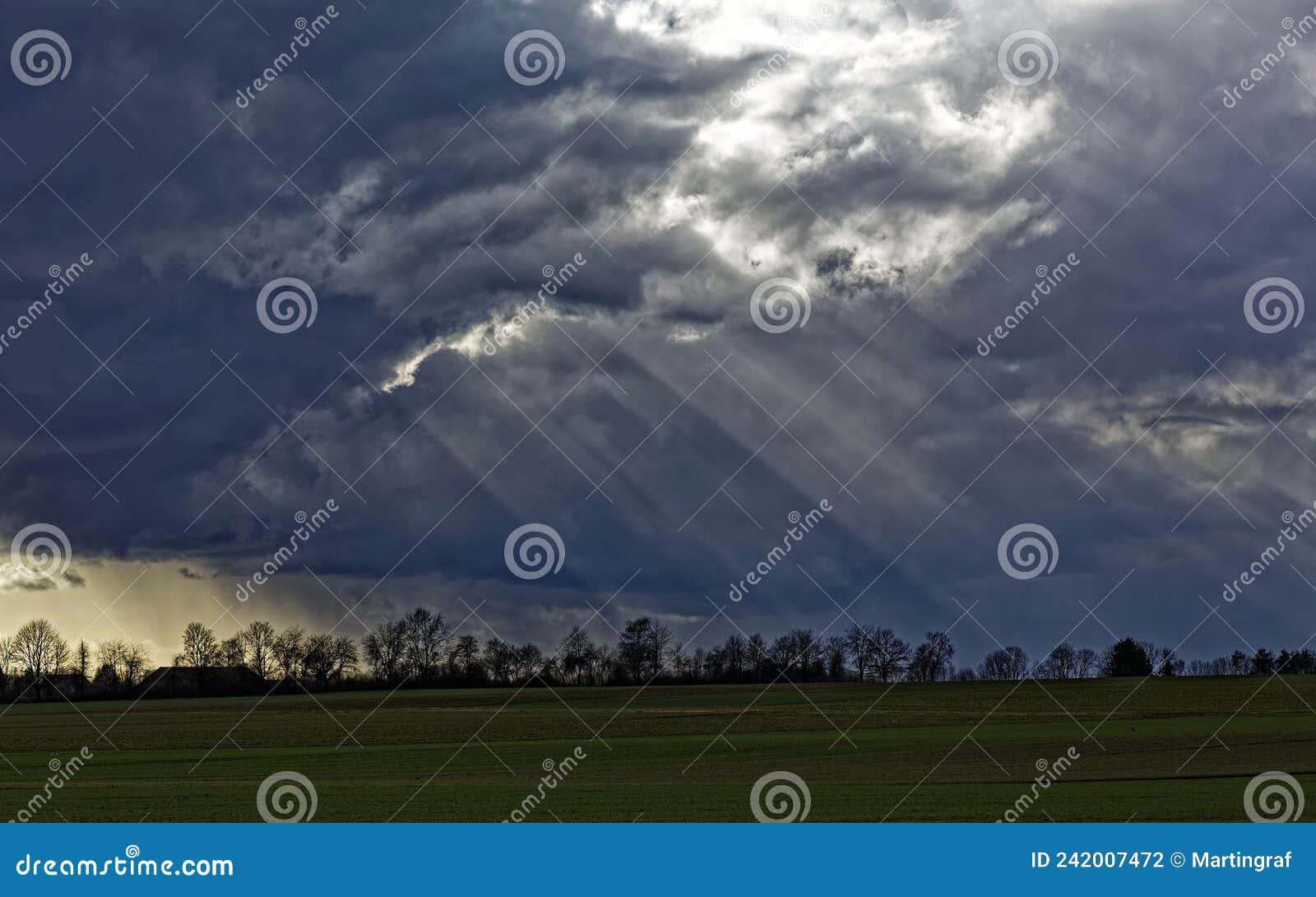 Sun Rays through Dark Clouds Over a Field and Shower in the Background ...