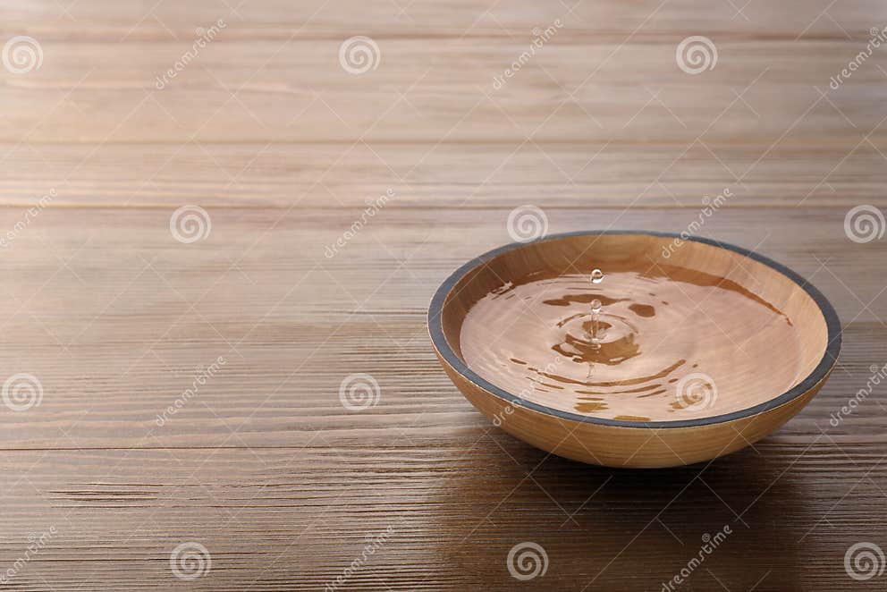 Drop Falling Down into Bowl with Clear Water on Wooden Table. Space for ...